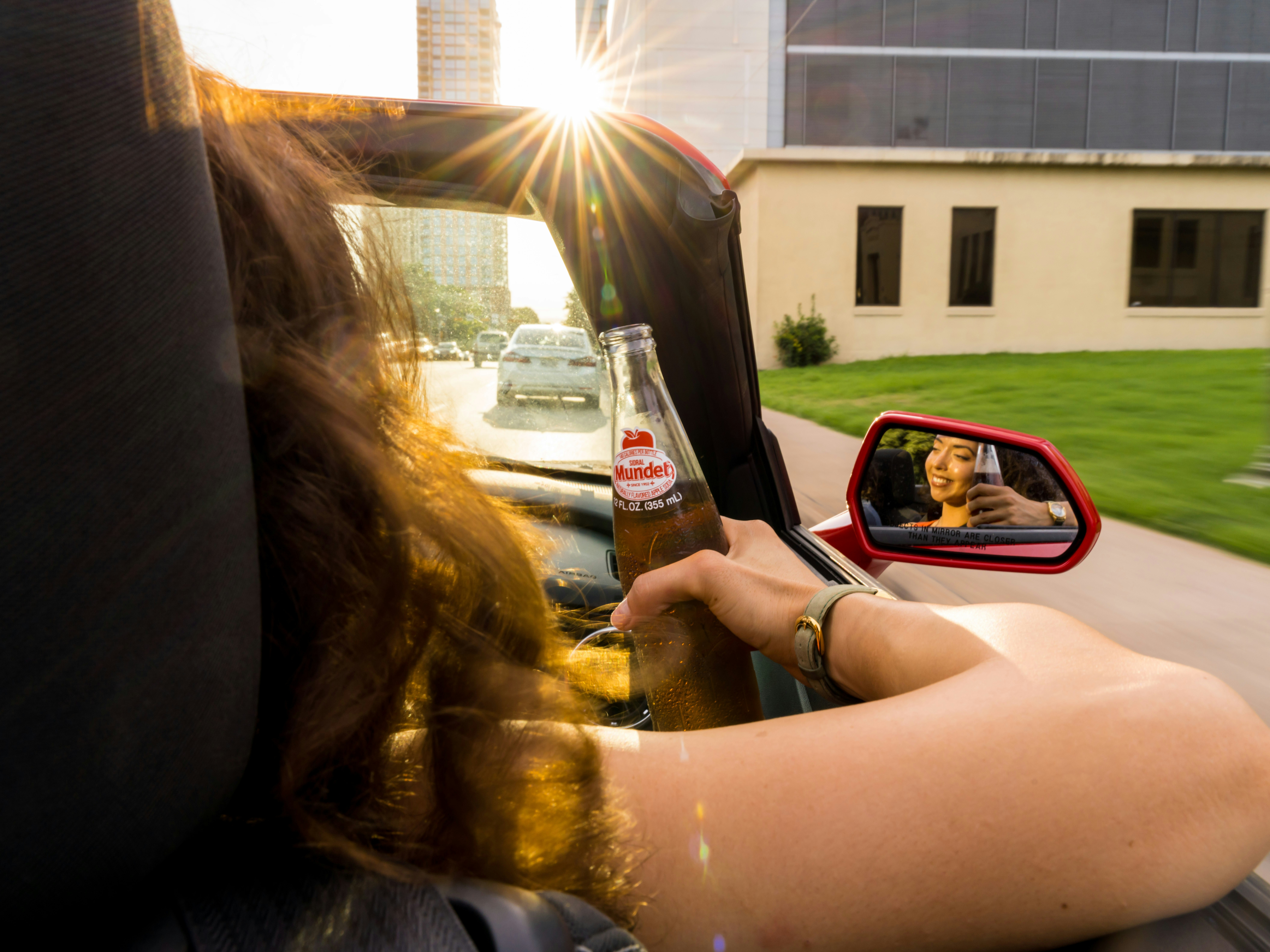 Sunlit Convertible Moment: A Hand, a Bottle, and a Reflective Smile