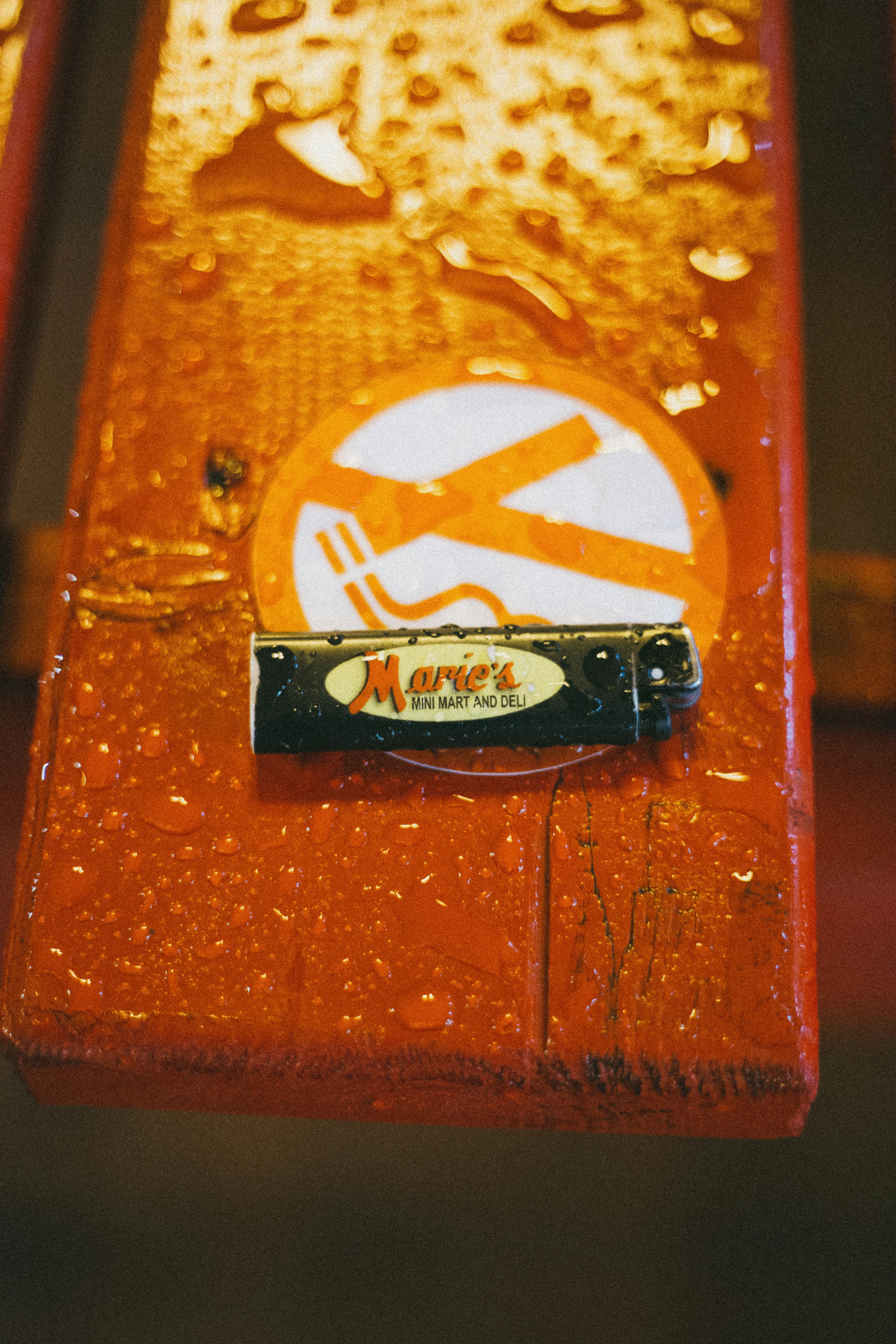 Red Latch Macro: Rain-kissed Wood and a Circular Orange-White Sticker Logo