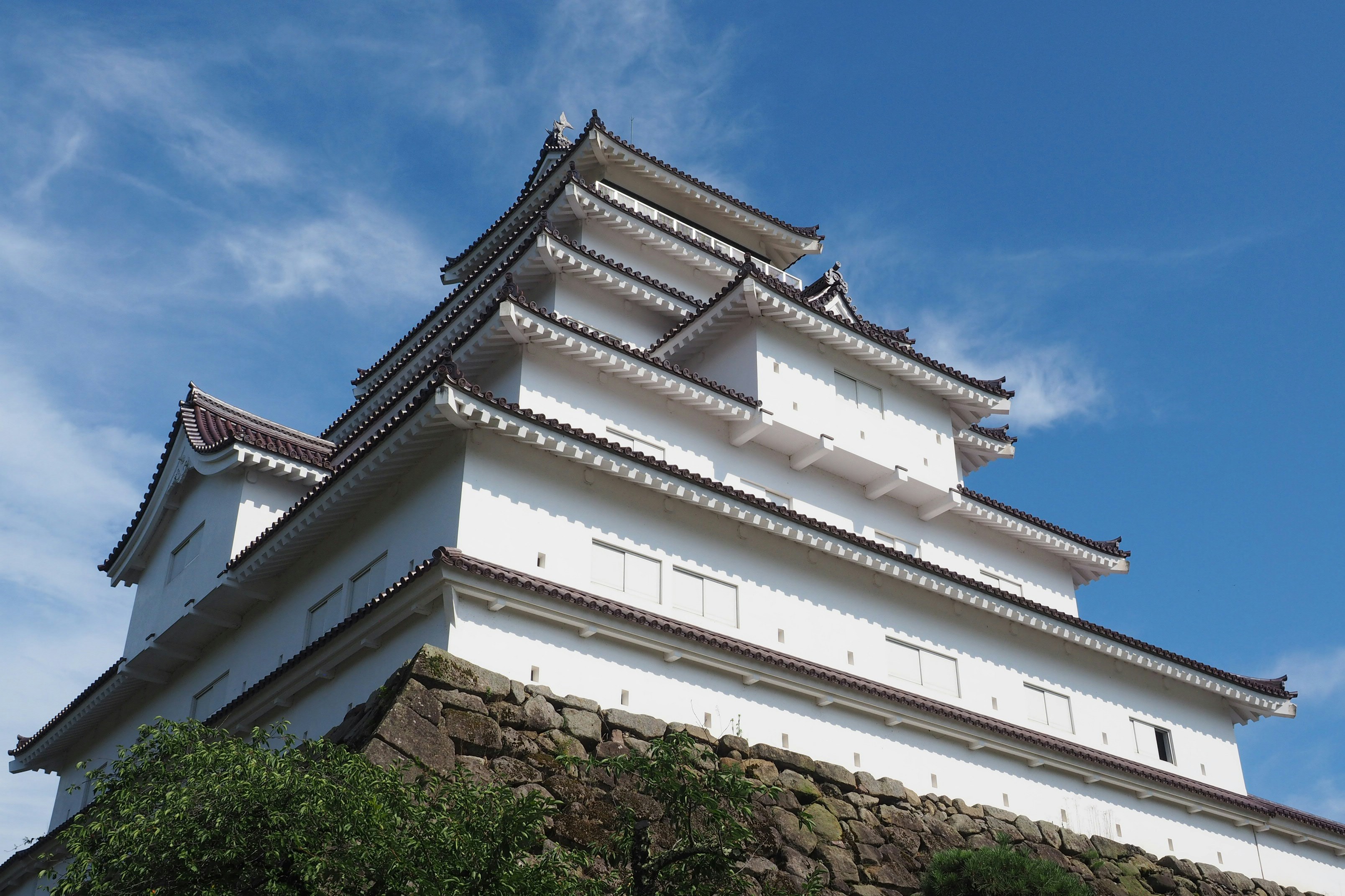 Historic Japanese castle perched on a rocky foundation, showcasing traditional architecture under a bright blue sky.