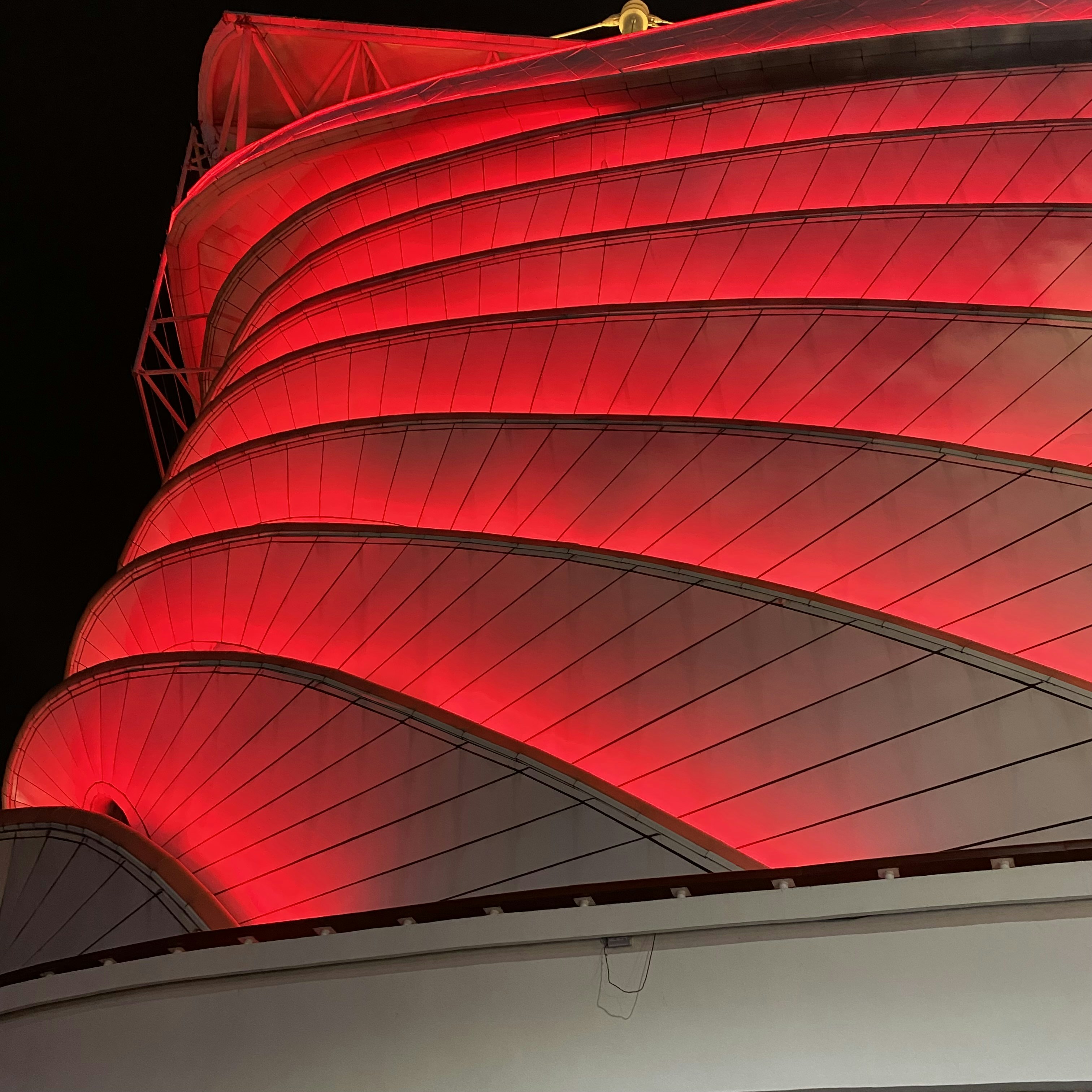 Dynamic architectural structure illuminated in vibrant red hues, showcasing a modern design against a night sky.