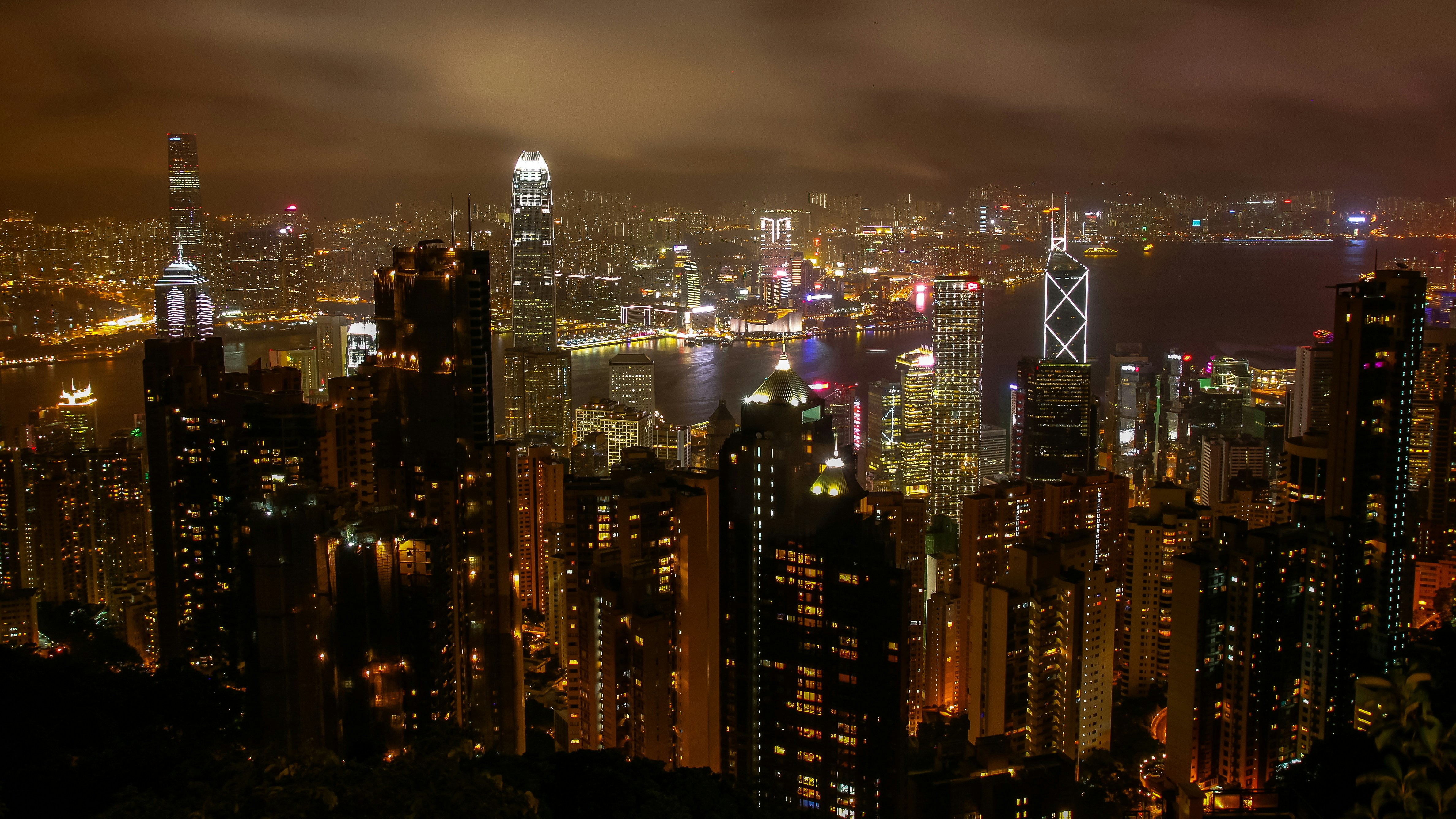 Vibrant cityscape of Hong Kong at night, showcasing a blend of skyscrapers and shimmering lights reflecting on the water. The scene captures the dynamic energy of urban life.