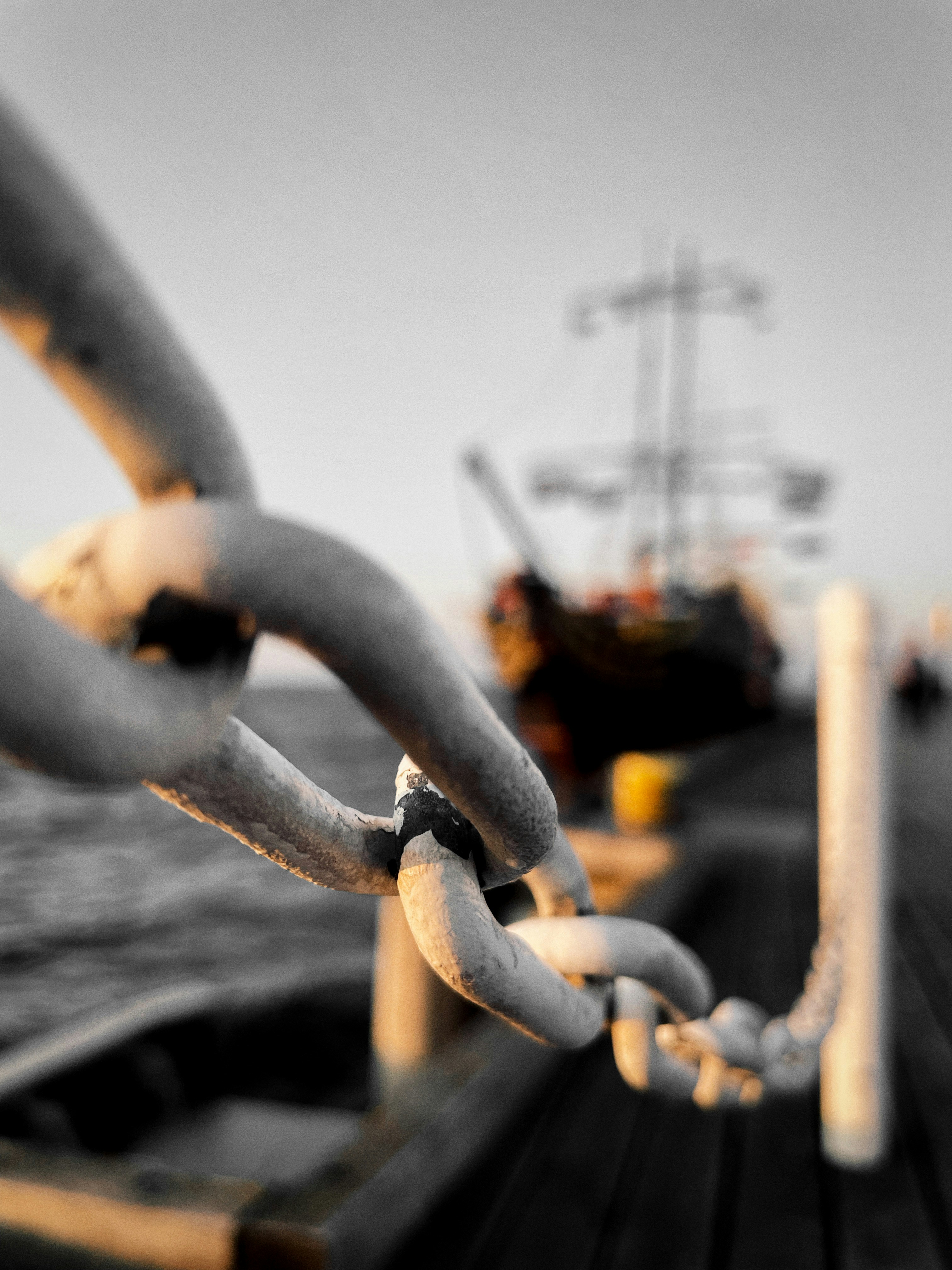 Close-up of a weathered chain leading towards a blurred ship on the horizon, evoking a sense of nostalgia and adventure.