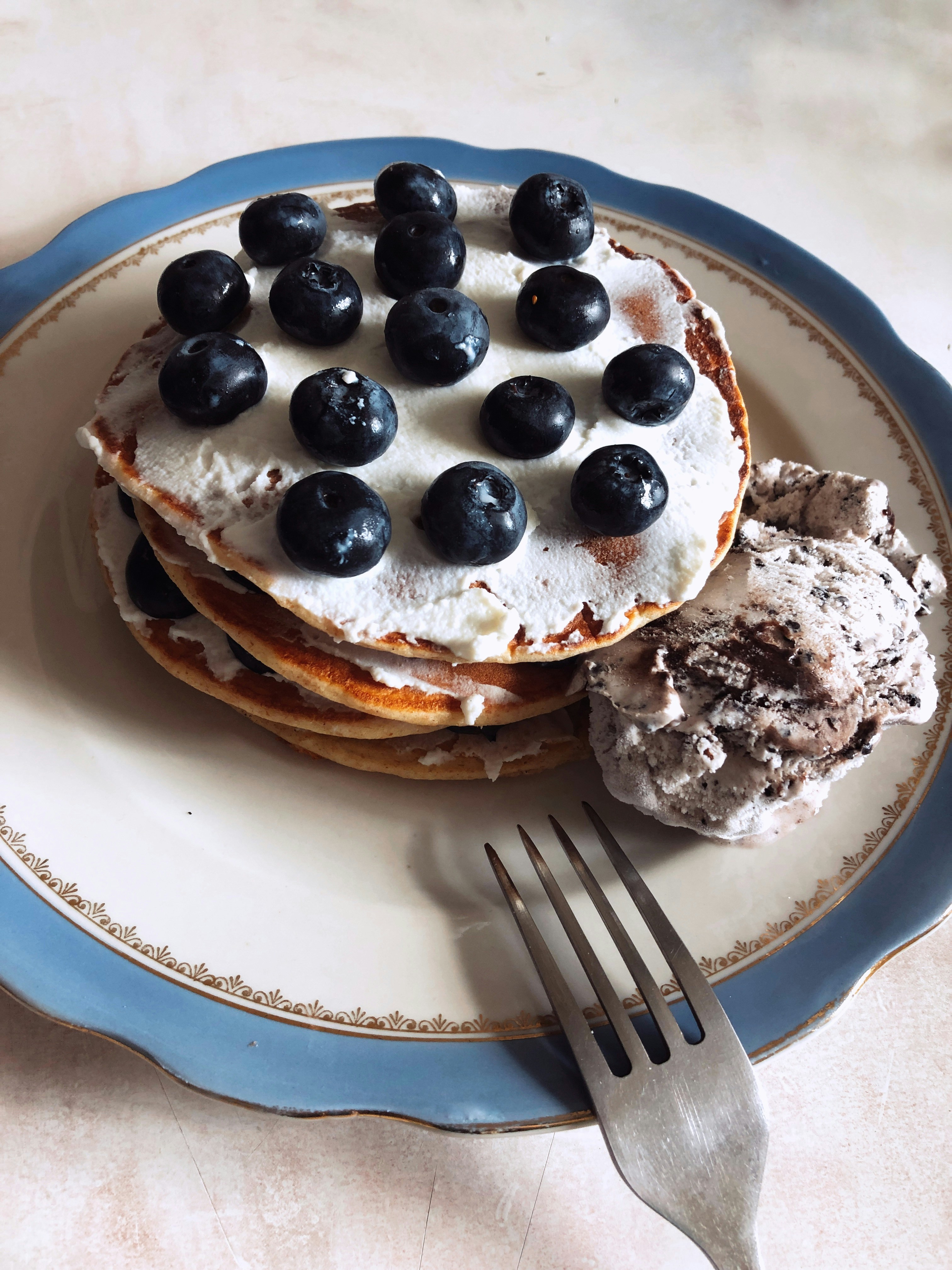 Stack of fluffy pancakes topped with whipped cream and fresh blueberries, accompanied by a scoop of chocolate ice cream.