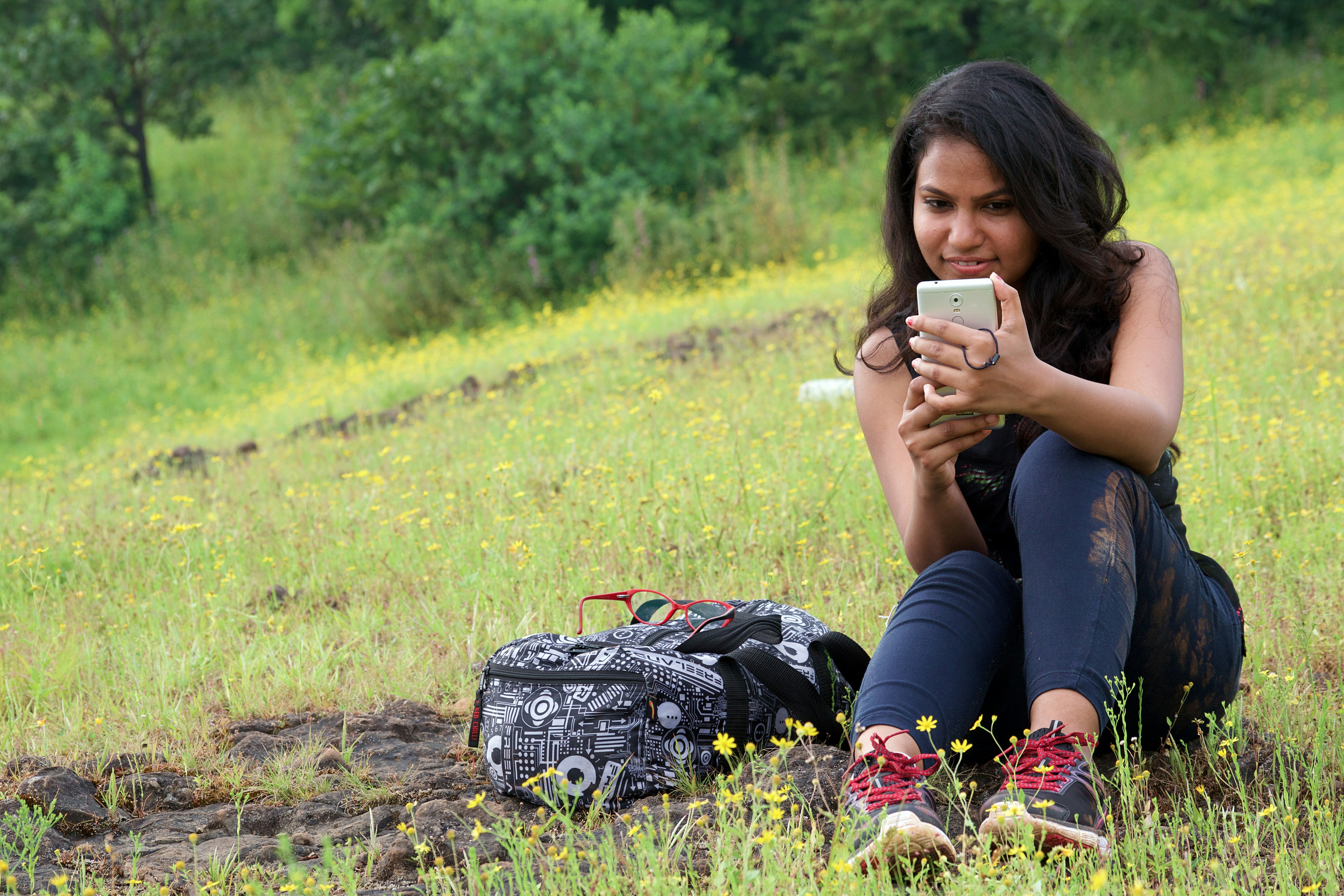 woman in black shirt and black pants sitting on grass field using smartphone