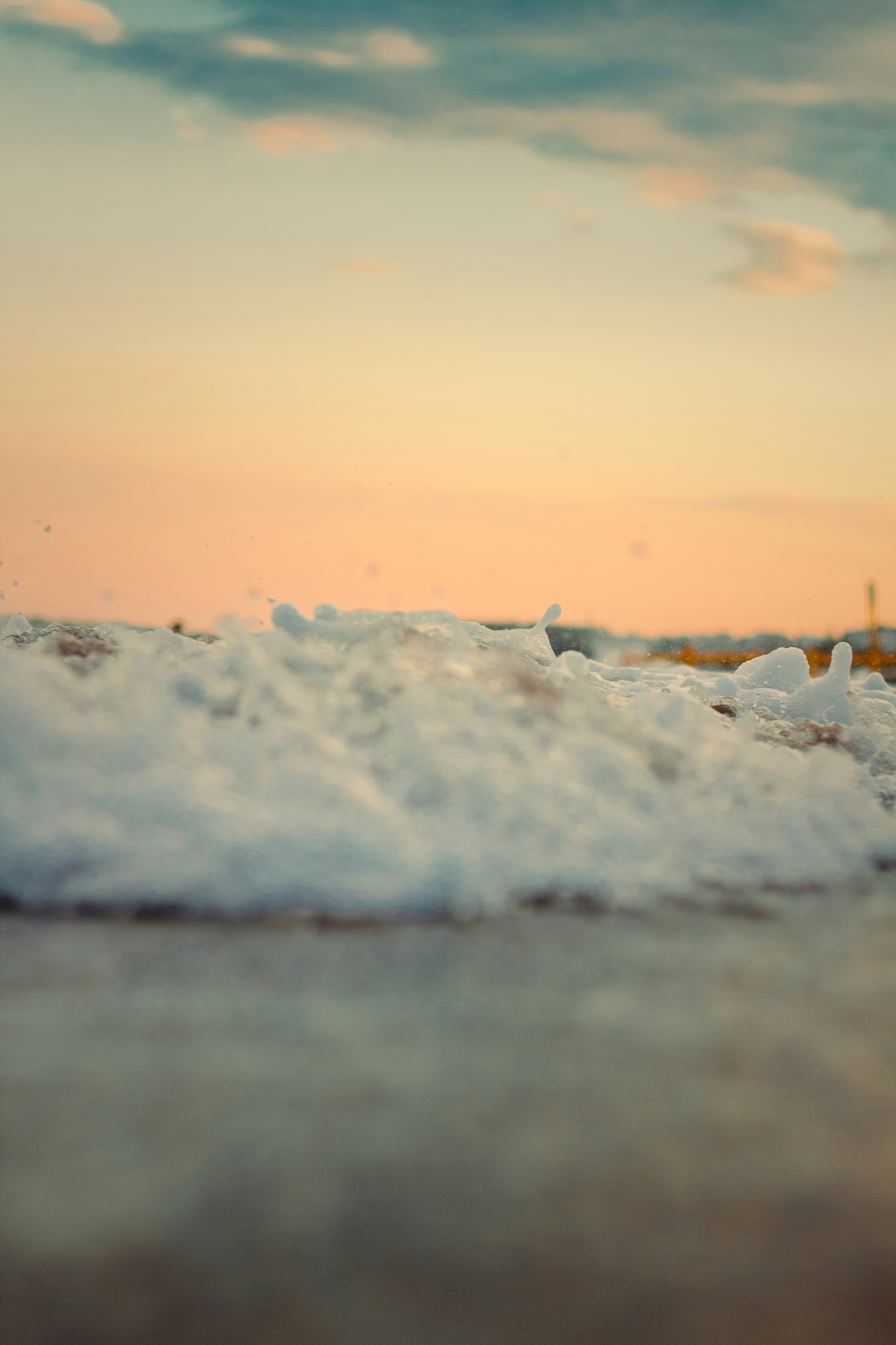 Foamy waves gently lap against the sandy beach at sunset, creating a serene atmosphere with pastel skies. 