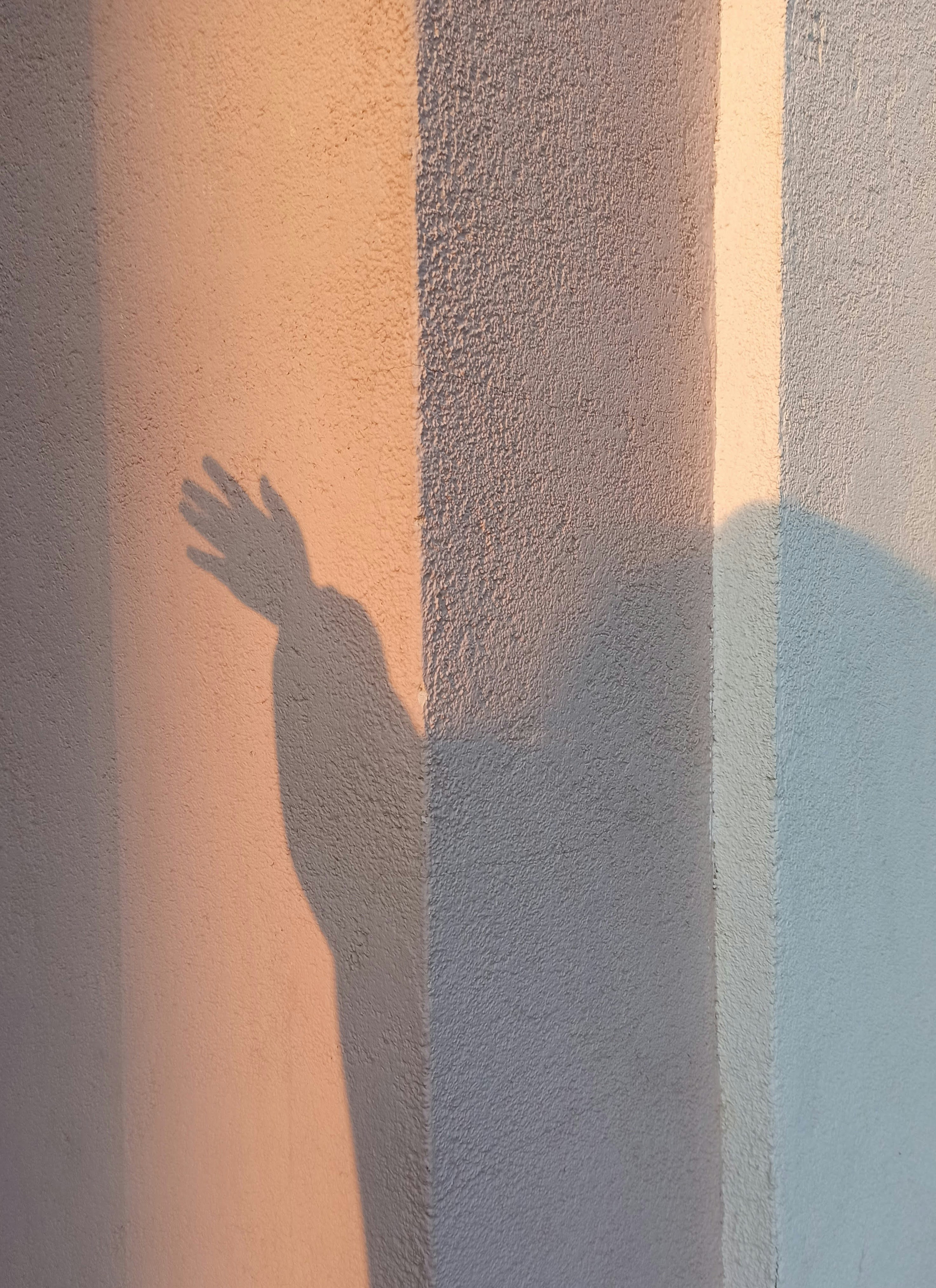 A hand silhouette cast against a textured wall, showcasing a blend of soft pastel colors in the background.