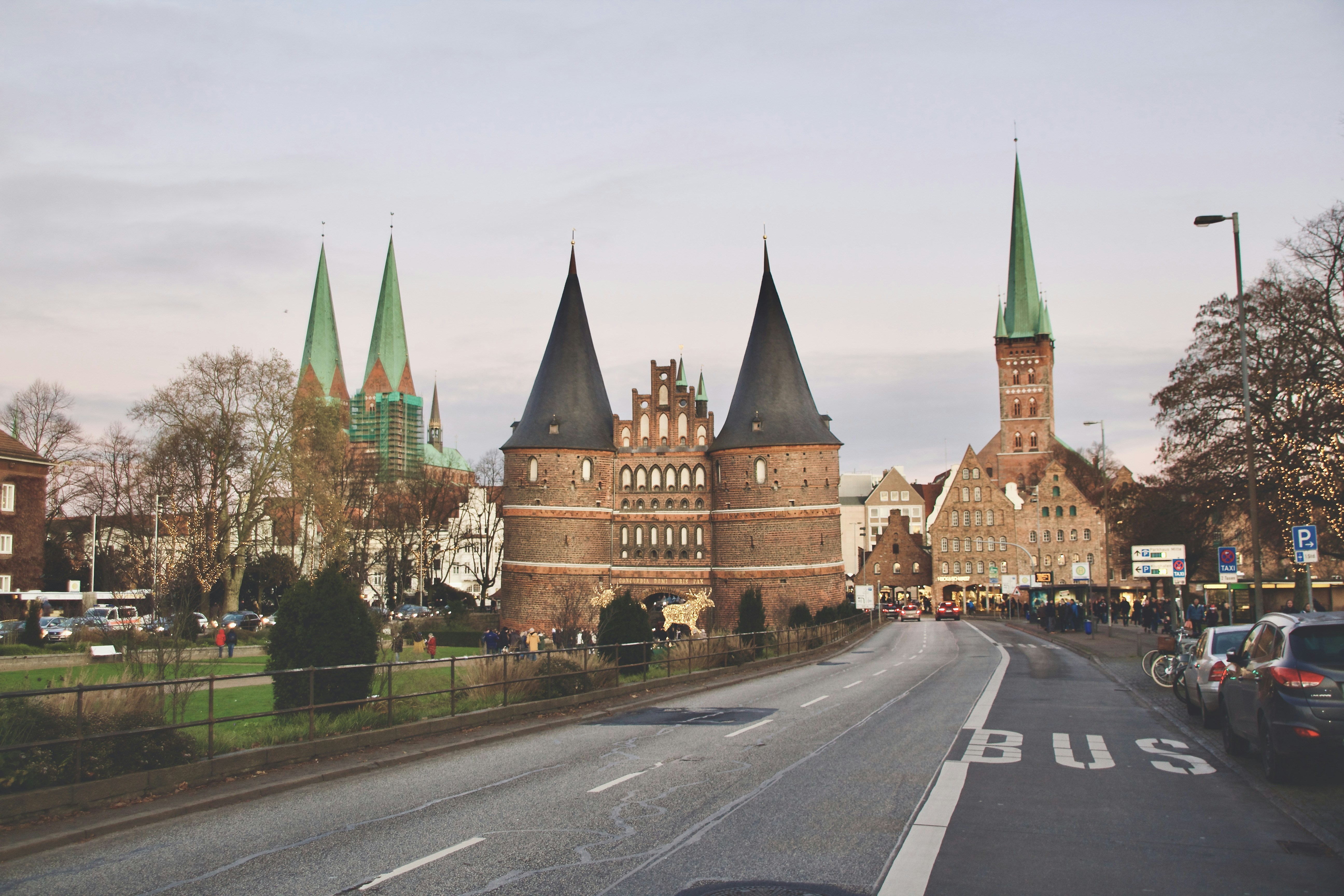 Historic brick gatehouse with pointed towers and green spires under a cloudy sky.