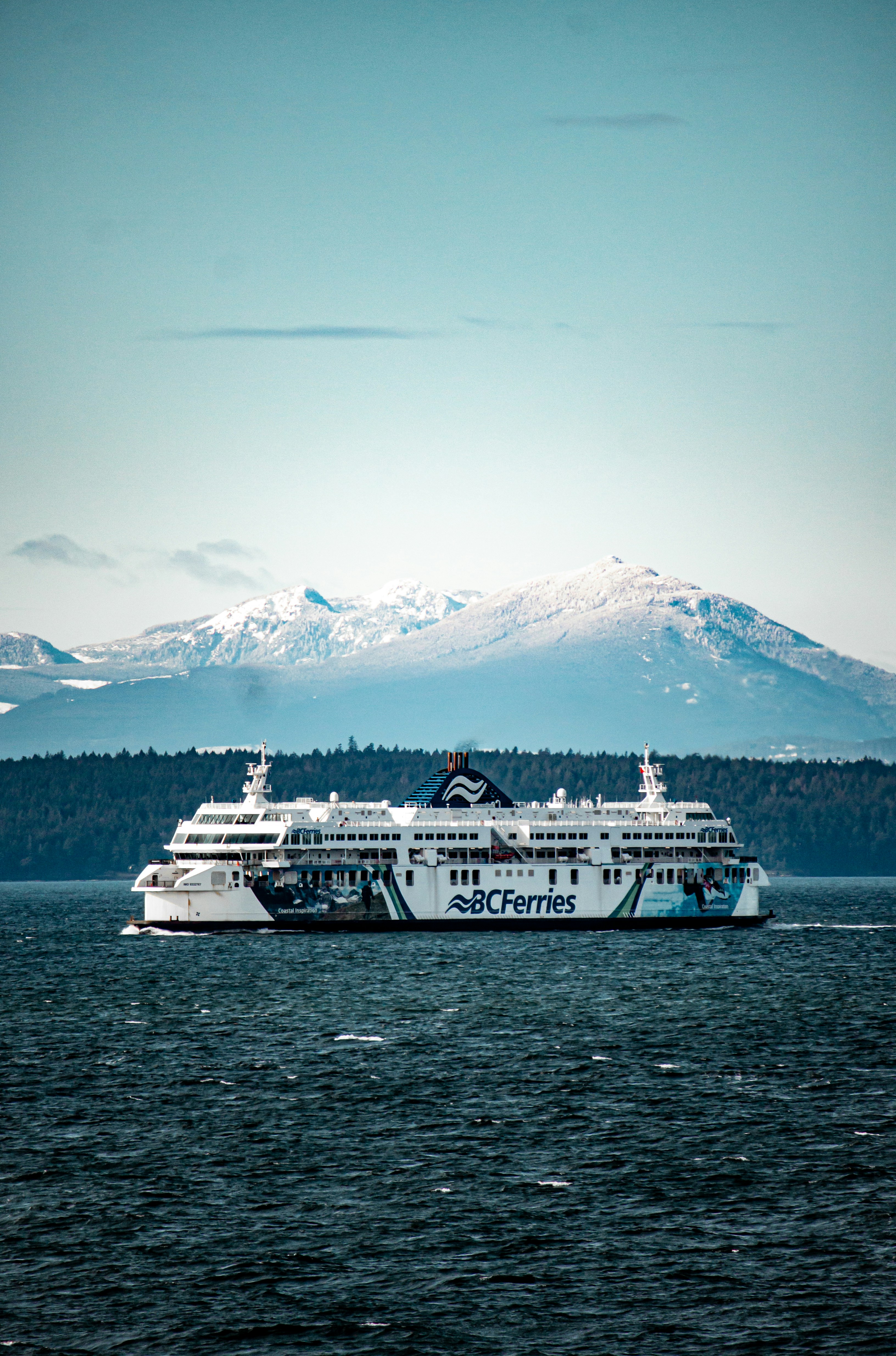 BC Ferries vessel gliding through the ocean with snow-capped mountains in the background, showcasing the beauty of coastal travel.