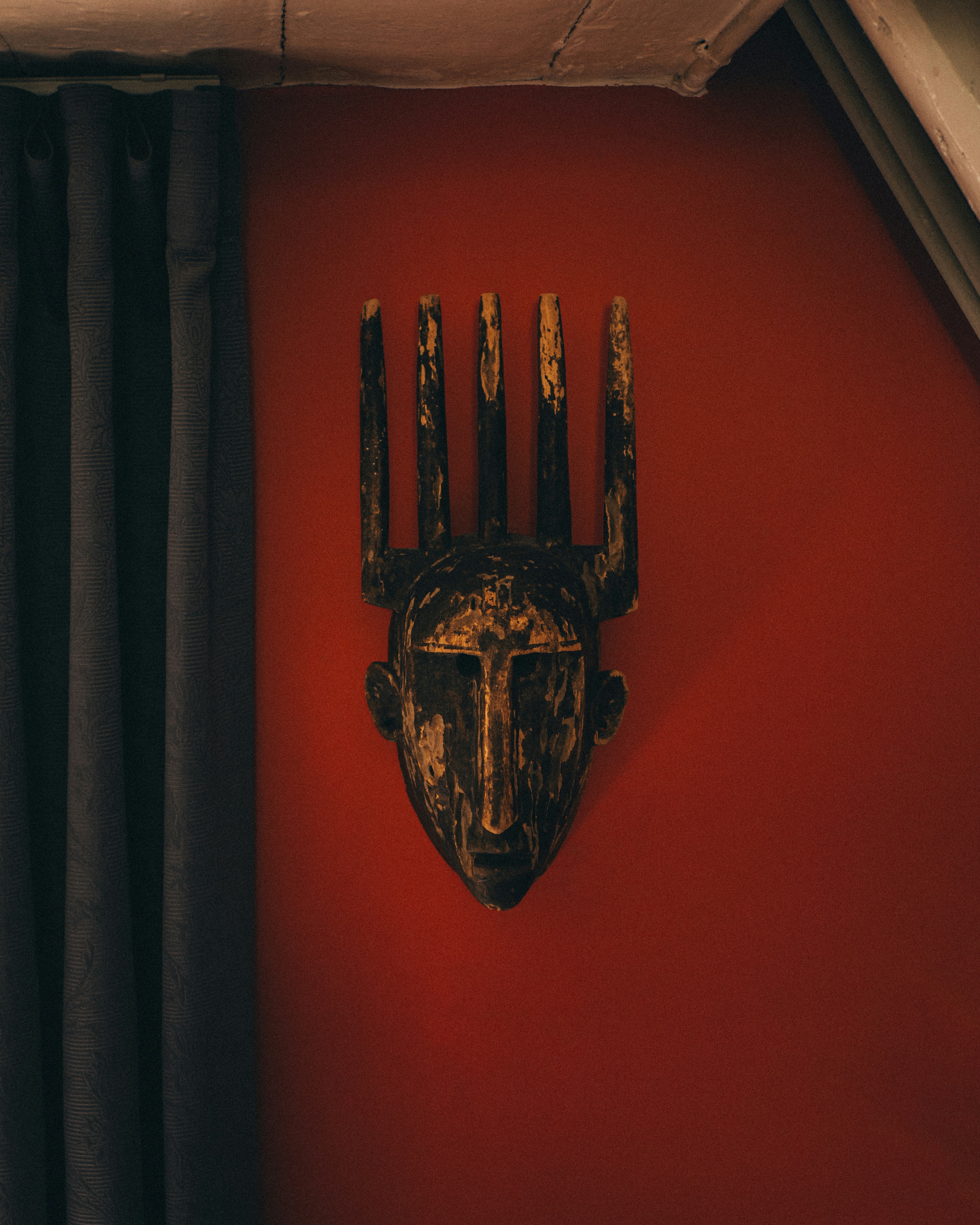 Crimson Sentinel: A Weathered Mask Reaching Toward the Ceiling