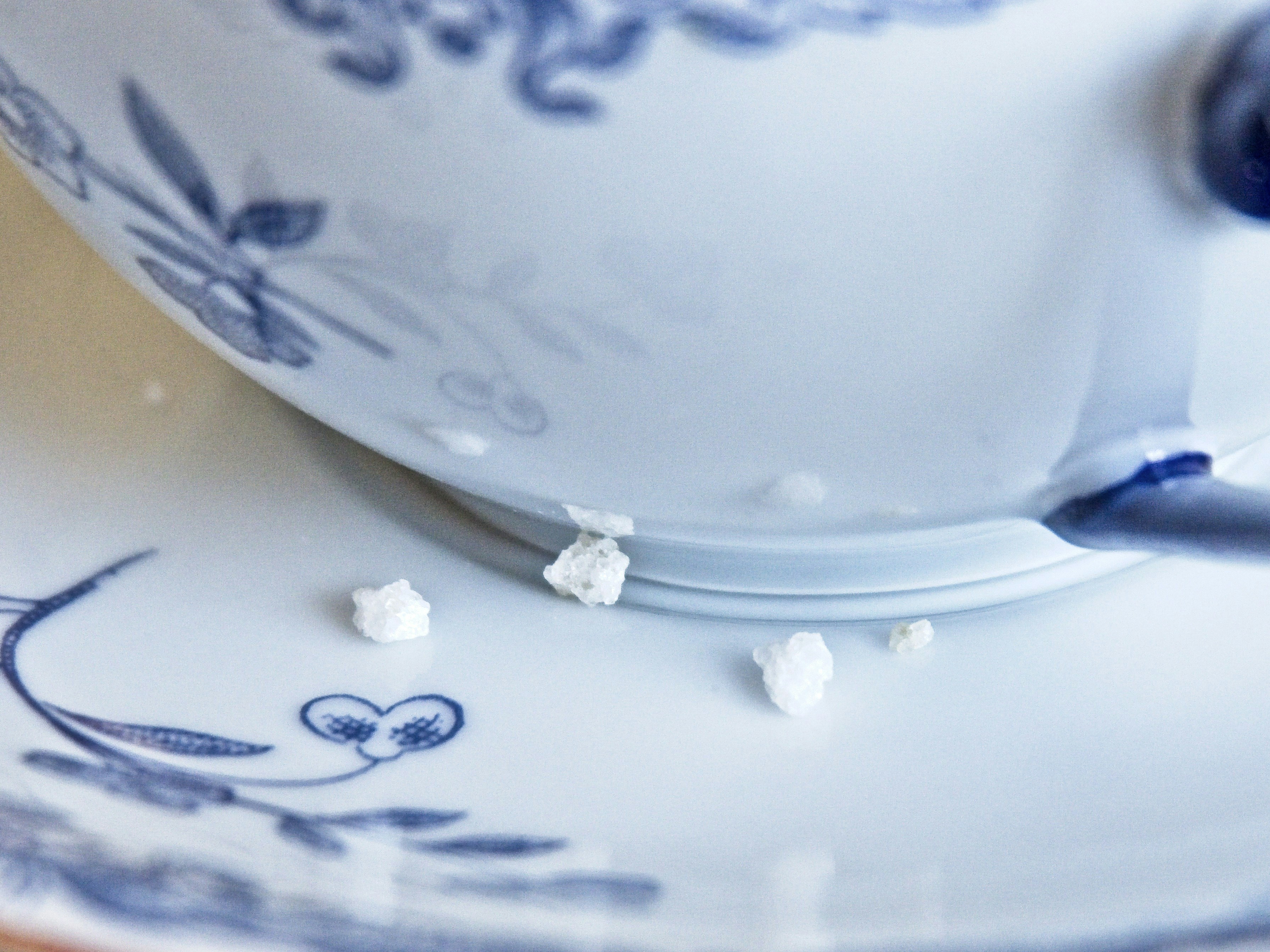Close-up photograph of a blue-and-white porcelain teacup and saucer with small salt crystals scattered on the surface.