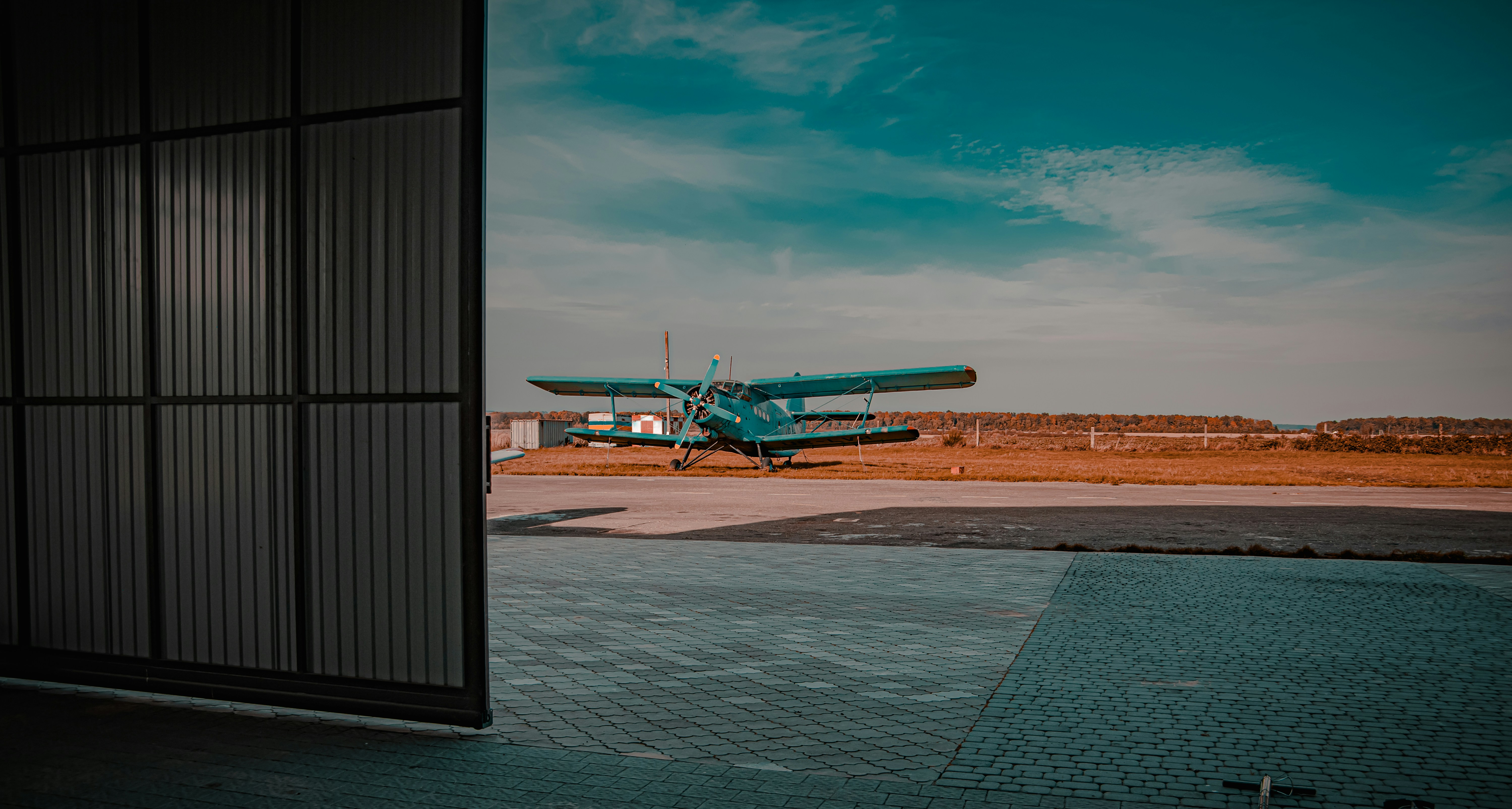 Vintage aircraft poised for departure, framed by the hangar's open doorway against a vibrant sky.