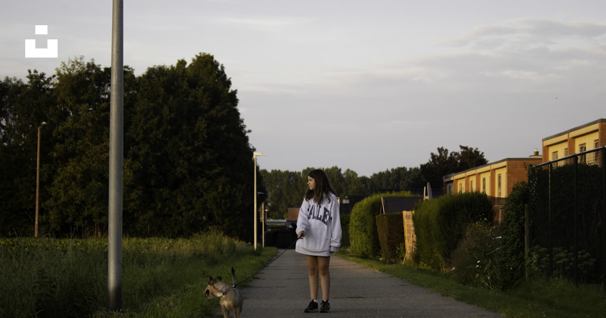 白いtシャツと青いデニムのショートパンツを着た女性が、白と茶色の犬を乗せて歩いているの写真 Unsplashの自然の画像の無料画像