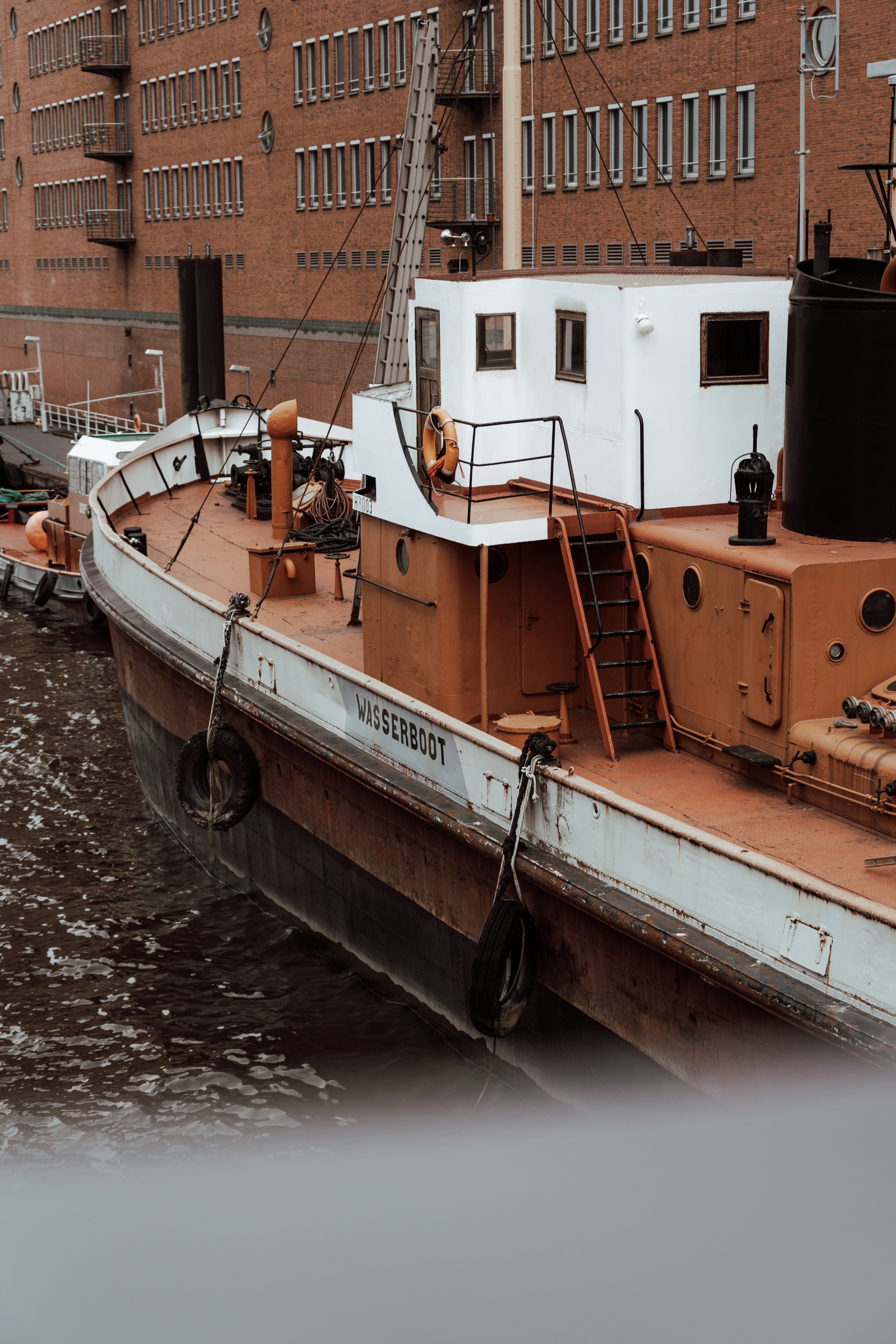 A vintage tugboat named Wasserboot docked beside a brick warehouse, showcasing industrial charm and maritime history.