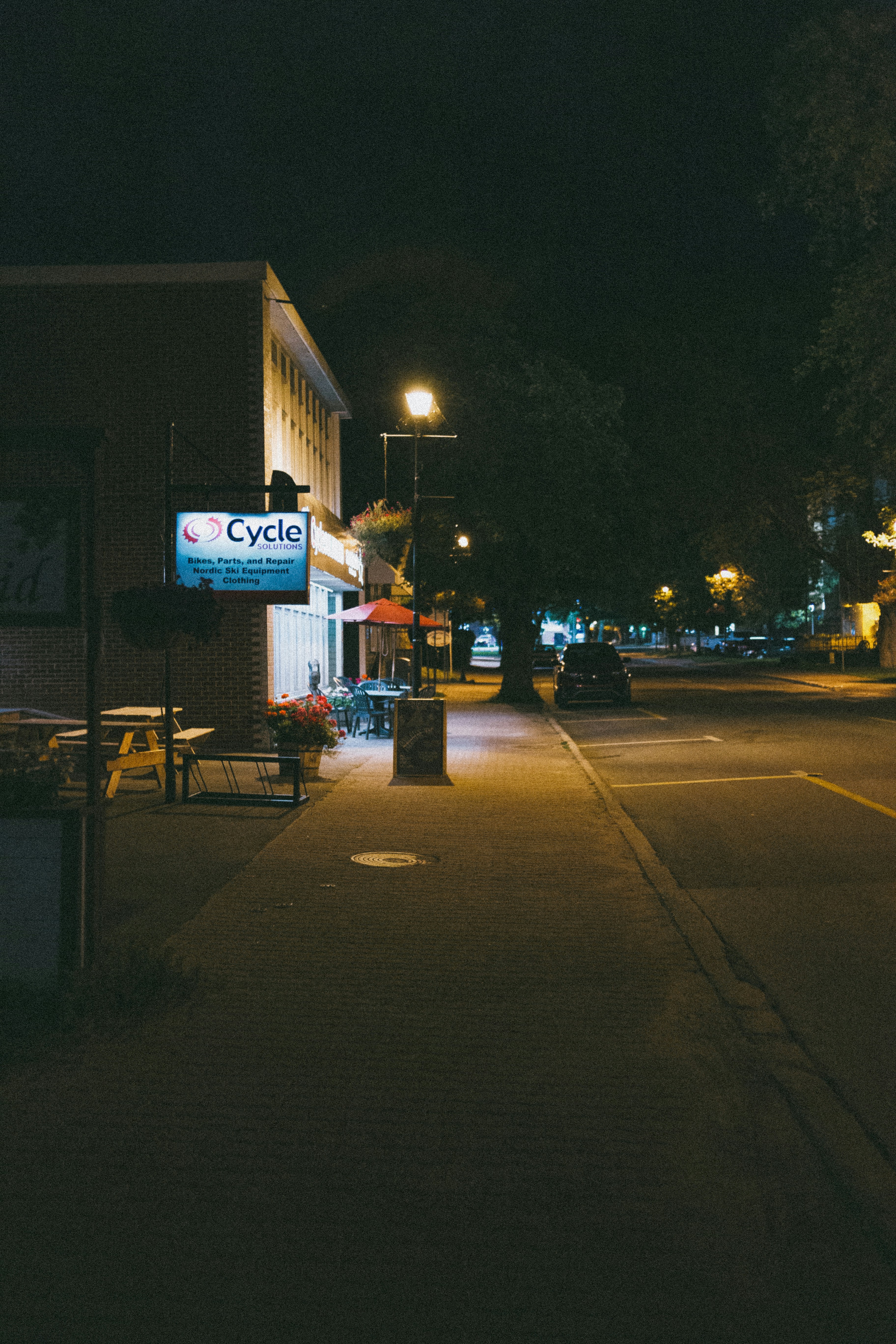 Street scene at night featuring a bicycle shop with illuminated signage and outdoor seating. The dimly lit street creates a serene atmosphere.