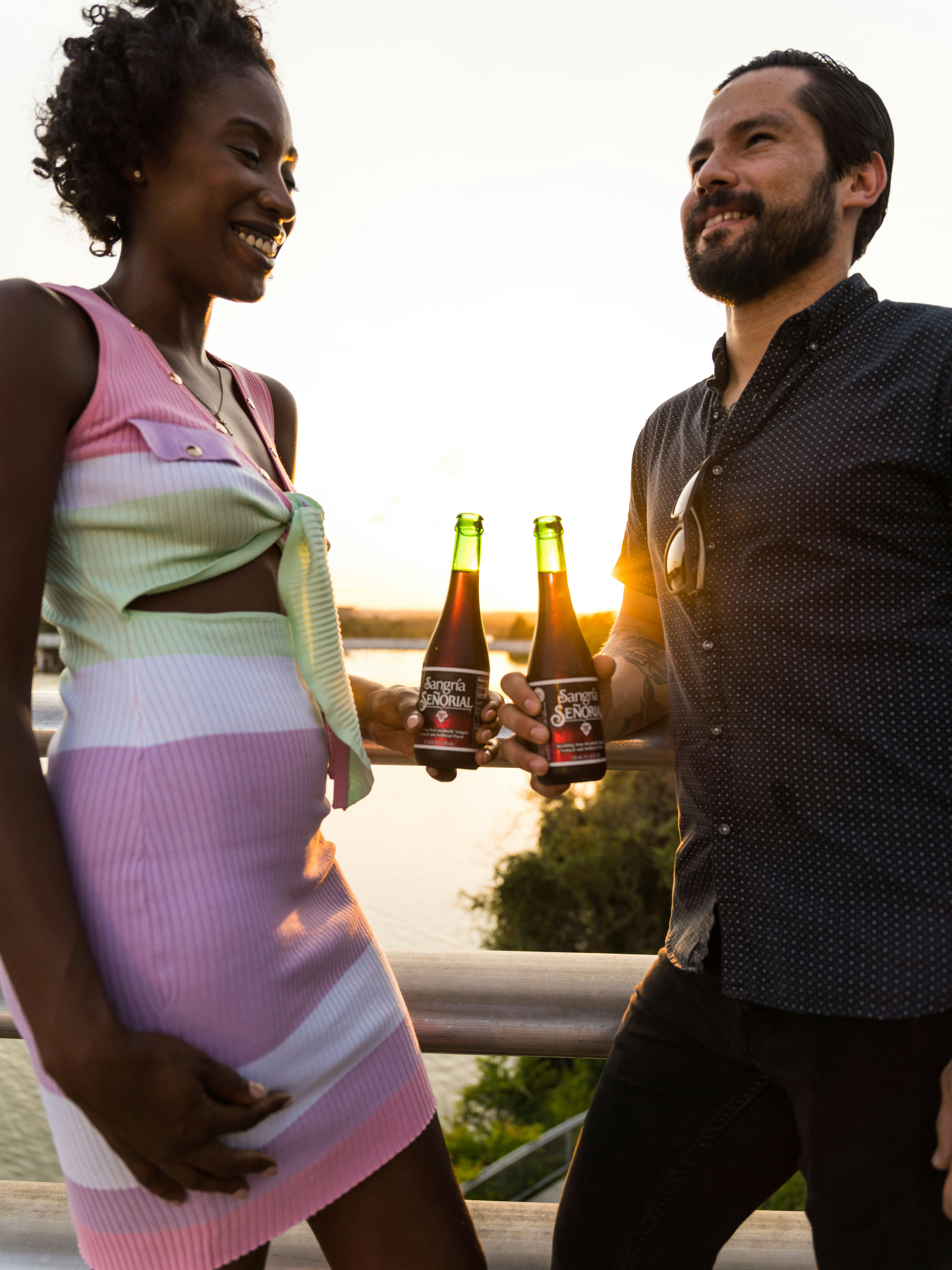 Amber Toast at Dusk: Friends Share a Sunset Moment Over the Bridge Rail