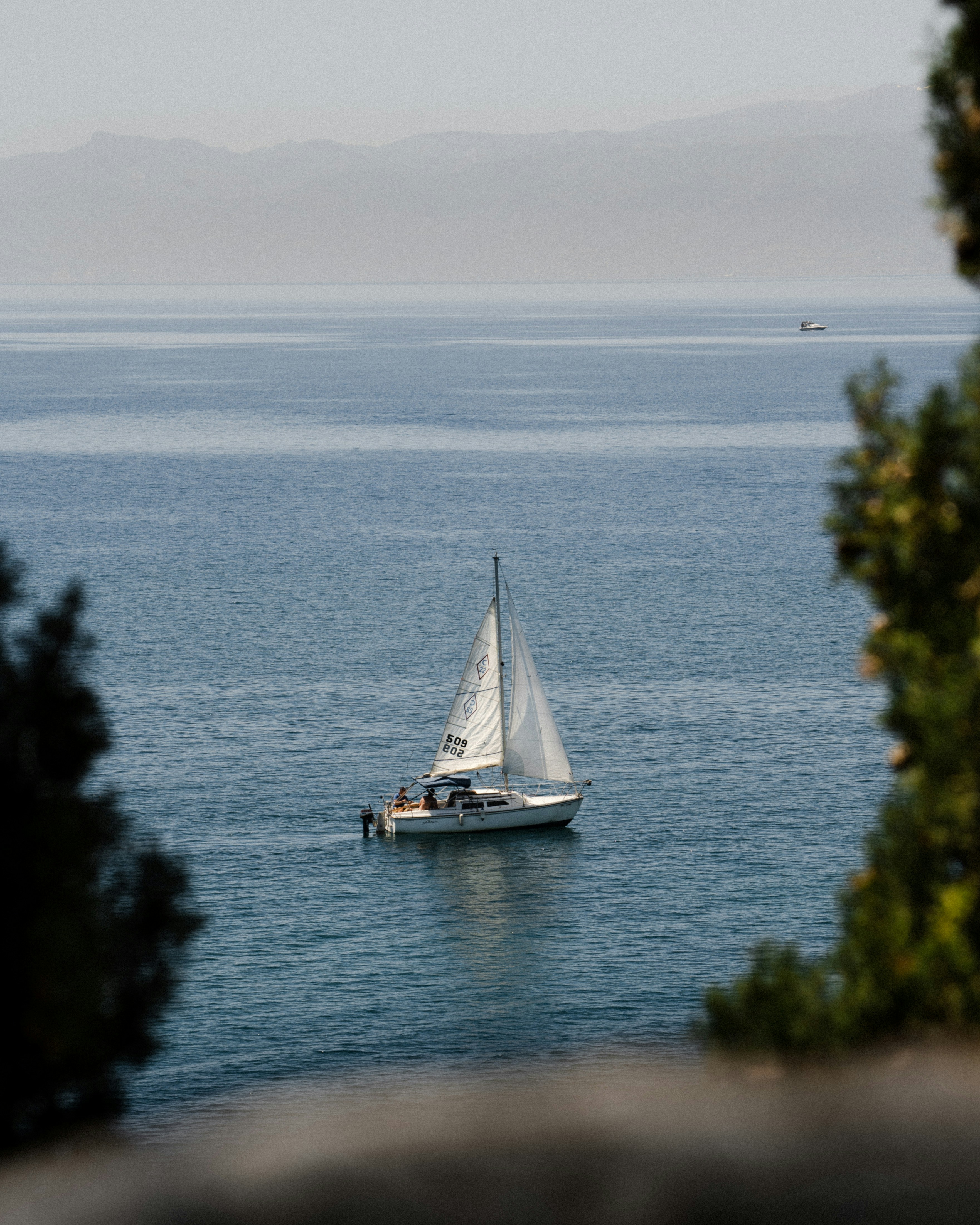 White sailboat gliding across a calm blue sea with distant mountains under a clear sky.