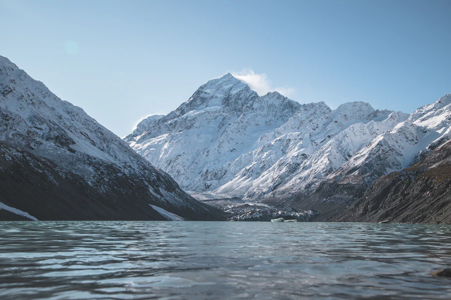 Snow-dusted mountains surround a calm fjord with a glassy surface; the scene emphasizes vast valley geometry and alpine light. A landscape photograph capturing alpine serenity and distant snow textures.