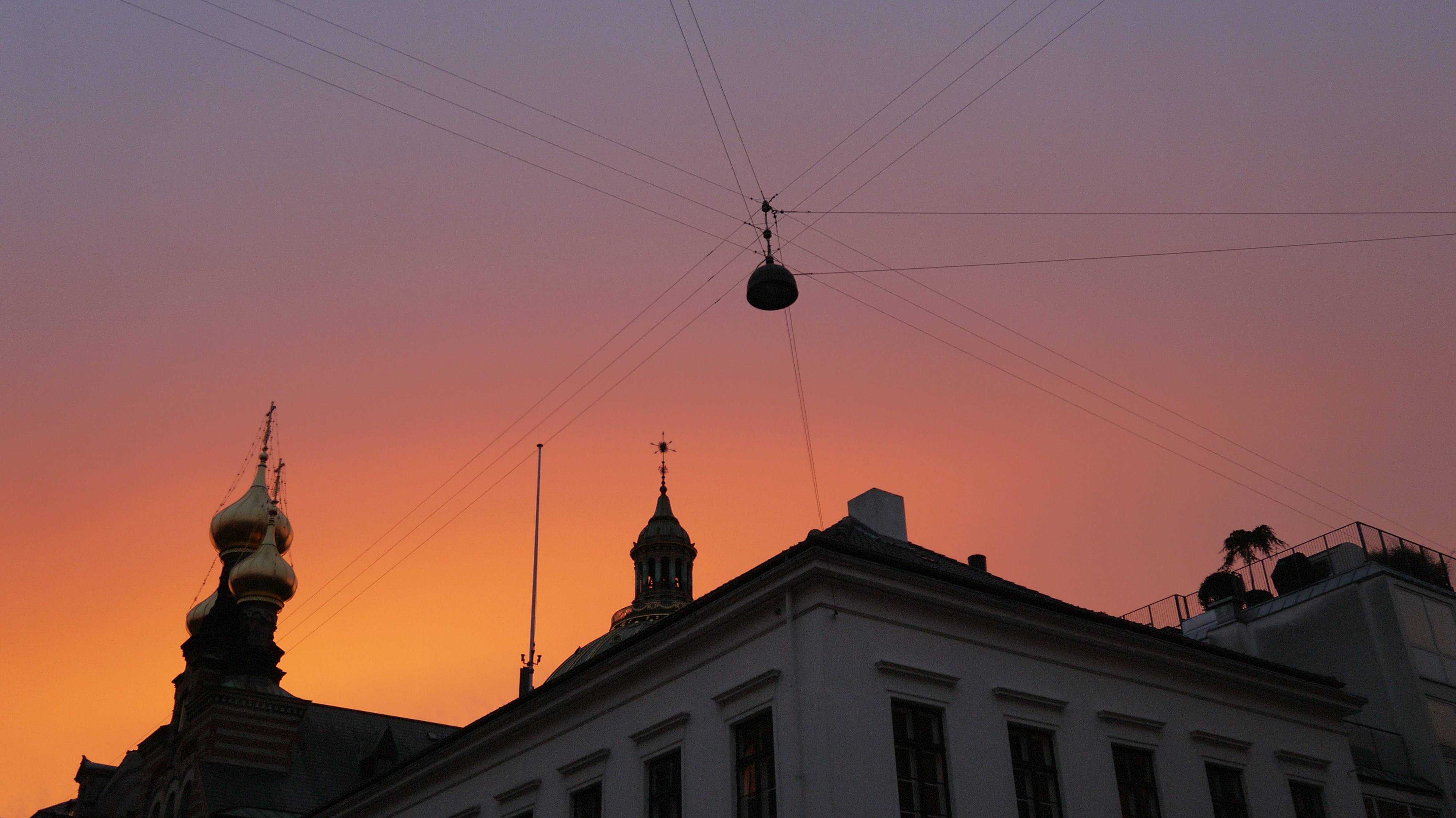 Historic architecture silhouetted against a vibrant twilight sky, highlighting ornate rooftops and a delicate web of overhead lines.