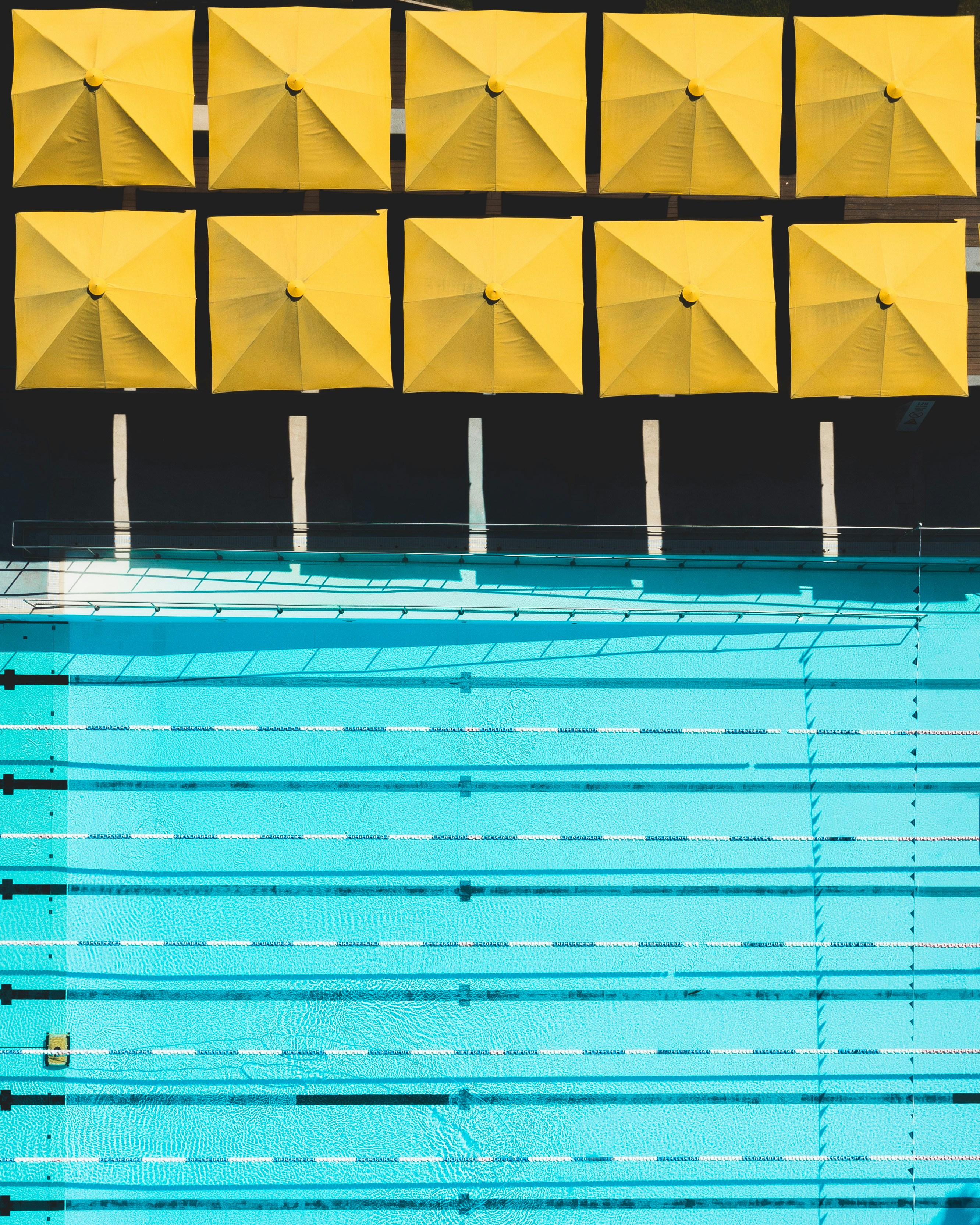 Sunlit Umbrella Grid Over a Turquoise Pool: An Aerial Pattern Study