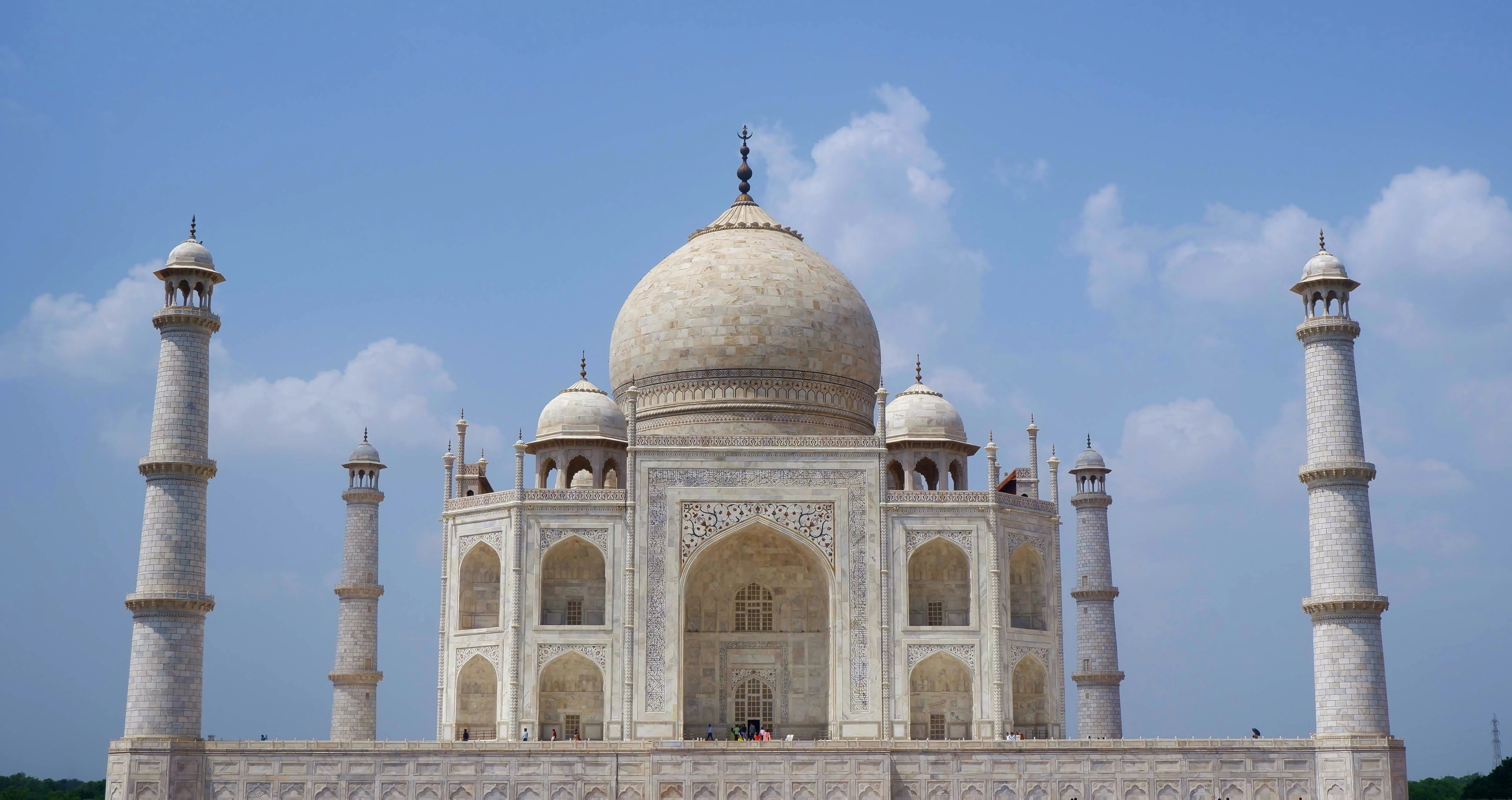 The Taj Mahal stands majestically under a clear blue sky, showcasing its intricate marble architecture and symmetrical minarets.