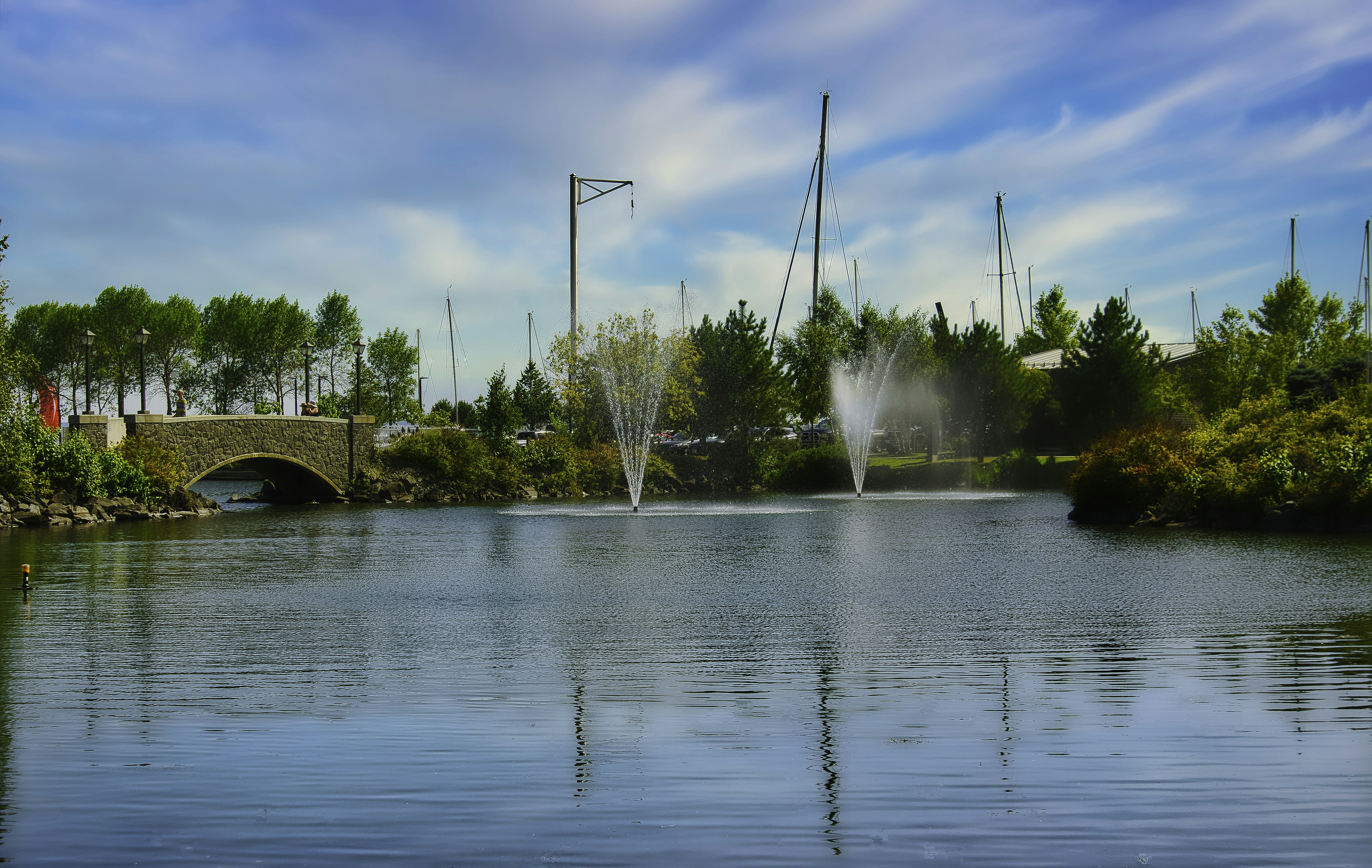 Centerpiece Fountains Over a Quiet Lake, Framed by a Stone Bridge and Distant Sail Masts