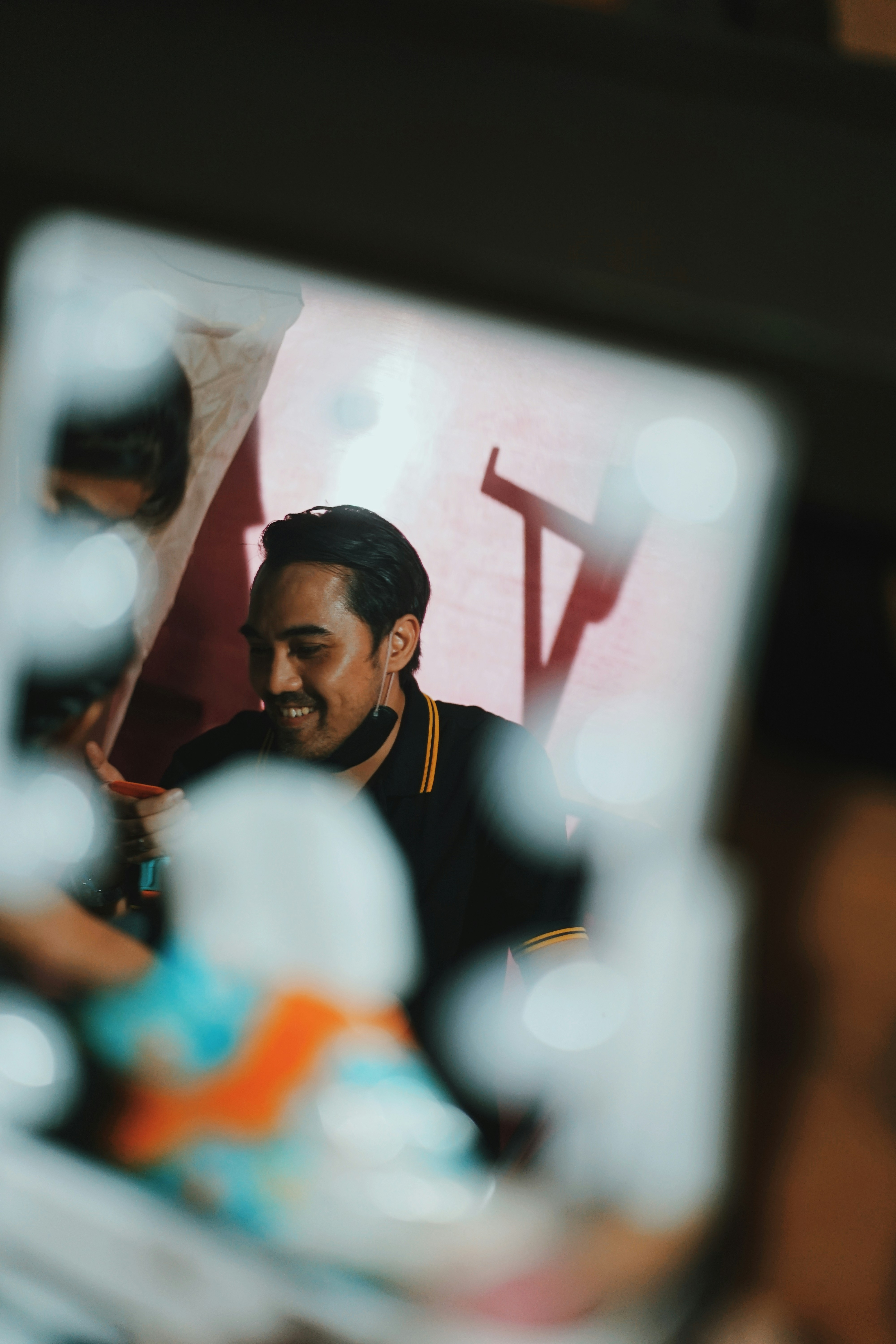 Person smiling in a mirror surrounded by soft lighting and blurred foreground.