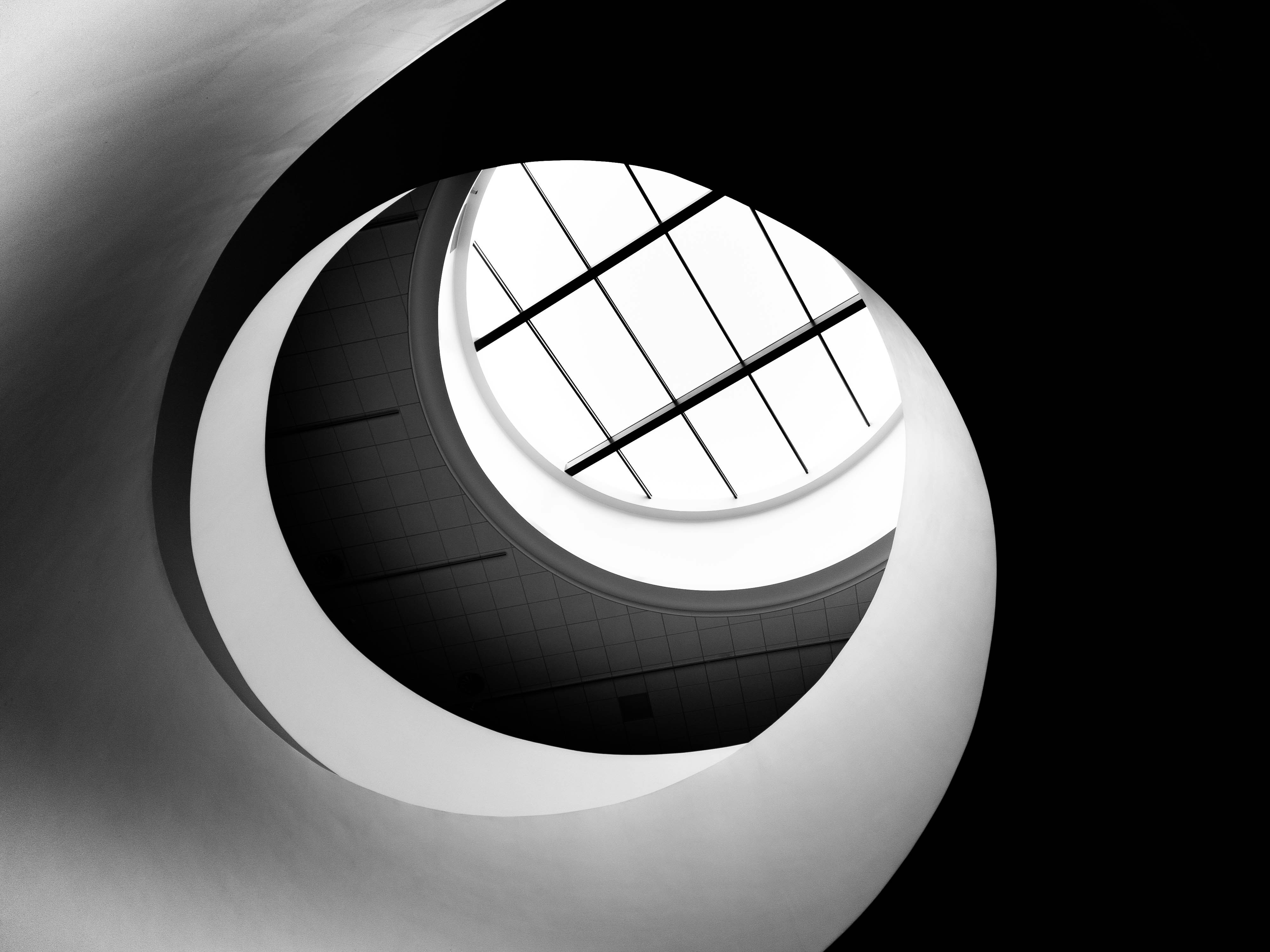 Abstract architectural spiral leading to a skylight, showcasing interplay between light and dark.