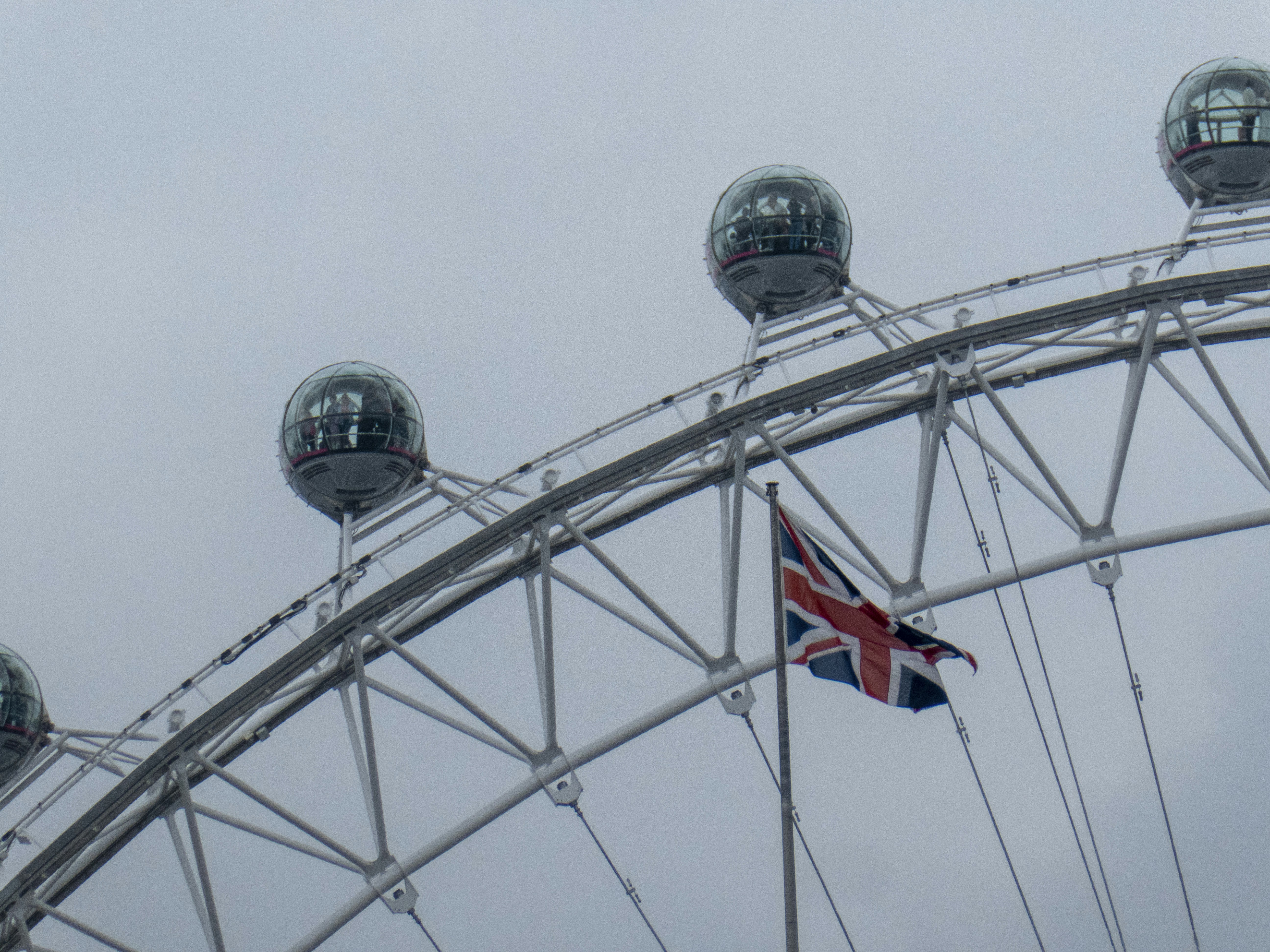 Flag Between Glass Orbs: A London Eye Arc in Pale Sky