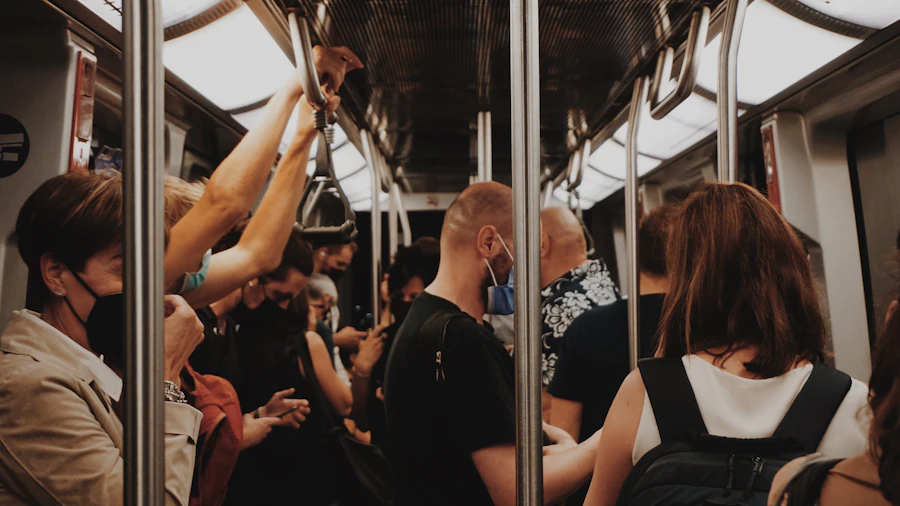 Commuters stand packed inside a subway car, holding overhead rails and facing different directions. Warm interior lighting and vertical poles create a tight, urban travel scene.
