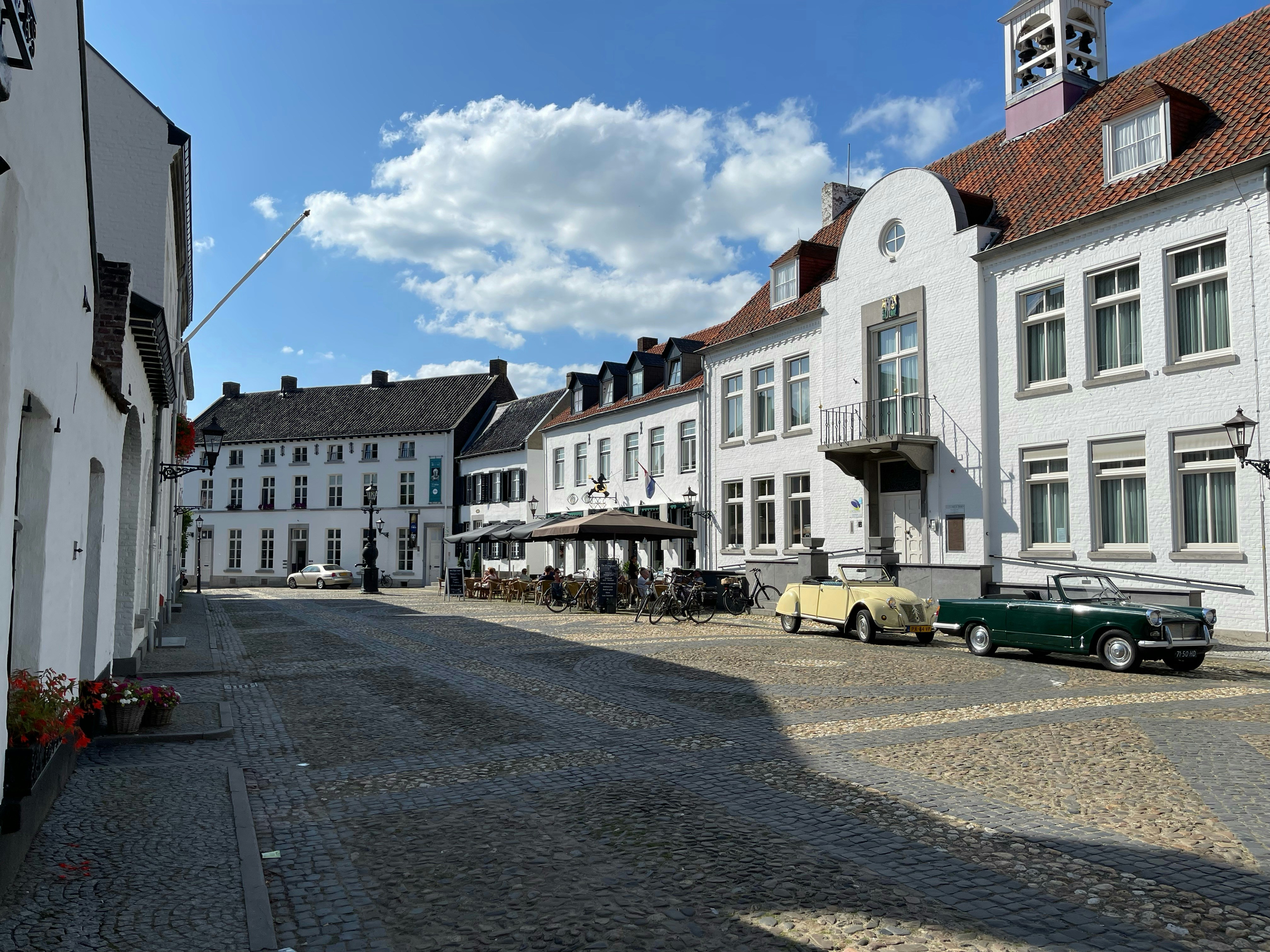 Historic cobblestone street lined with elegant buildings and classic cars under a vibrant sky.
