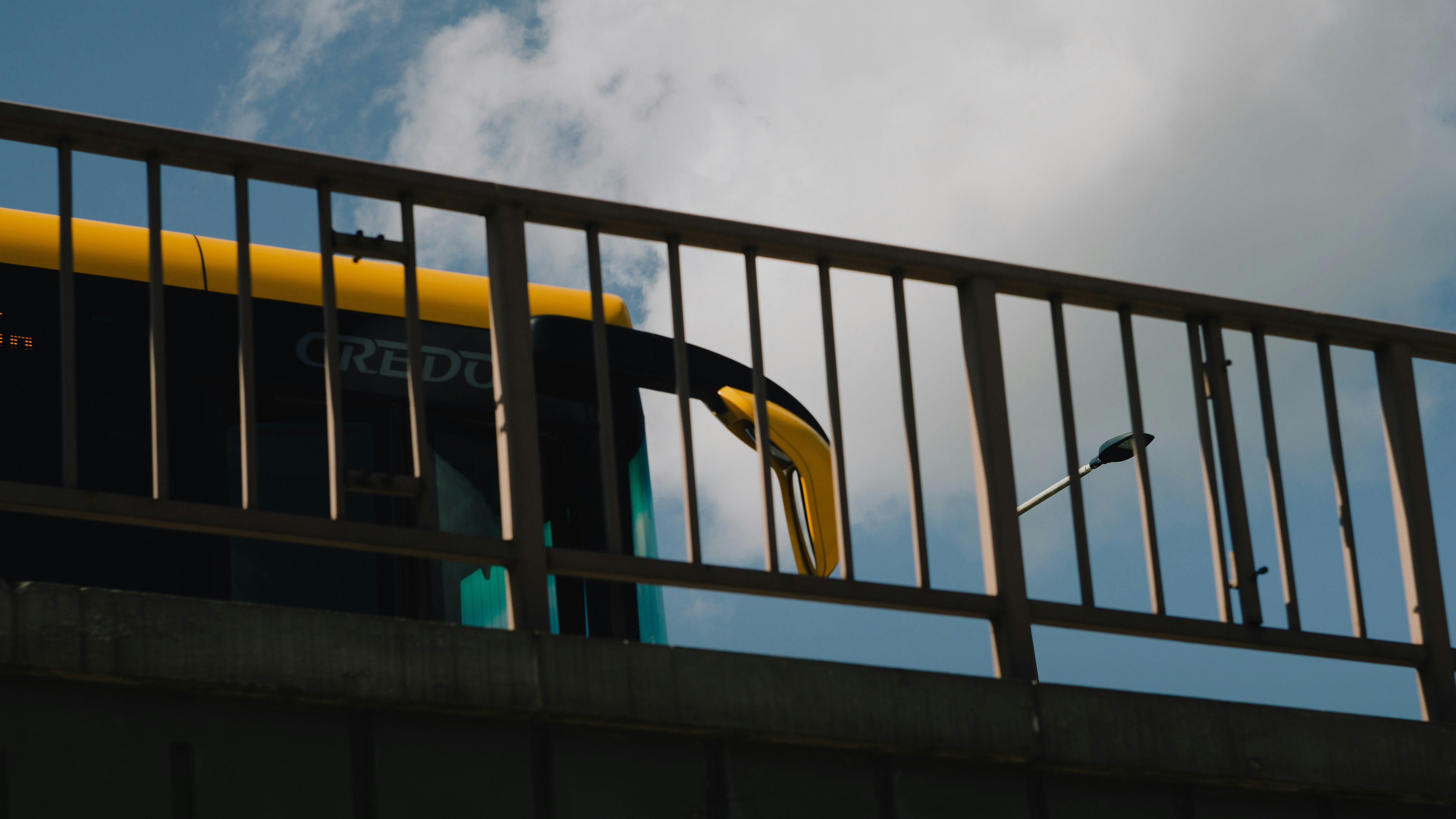 Yellow-Bodied Bus Overlooking a Guardrail under a Patchwork Sky
