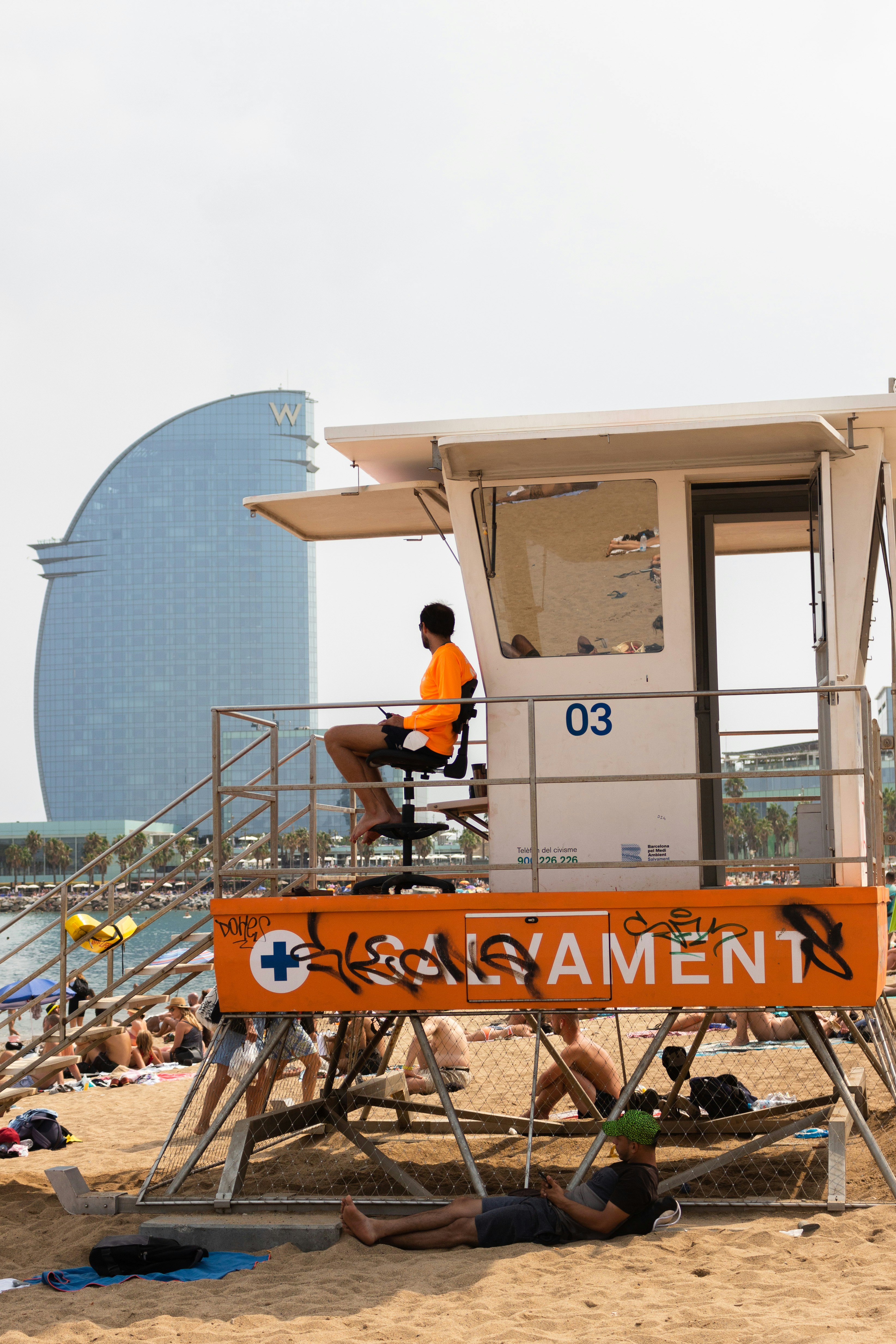 Lifeguard on Duty: Orange Uniform Over a Busy Barcelona Beach with the W Hotel in the Background