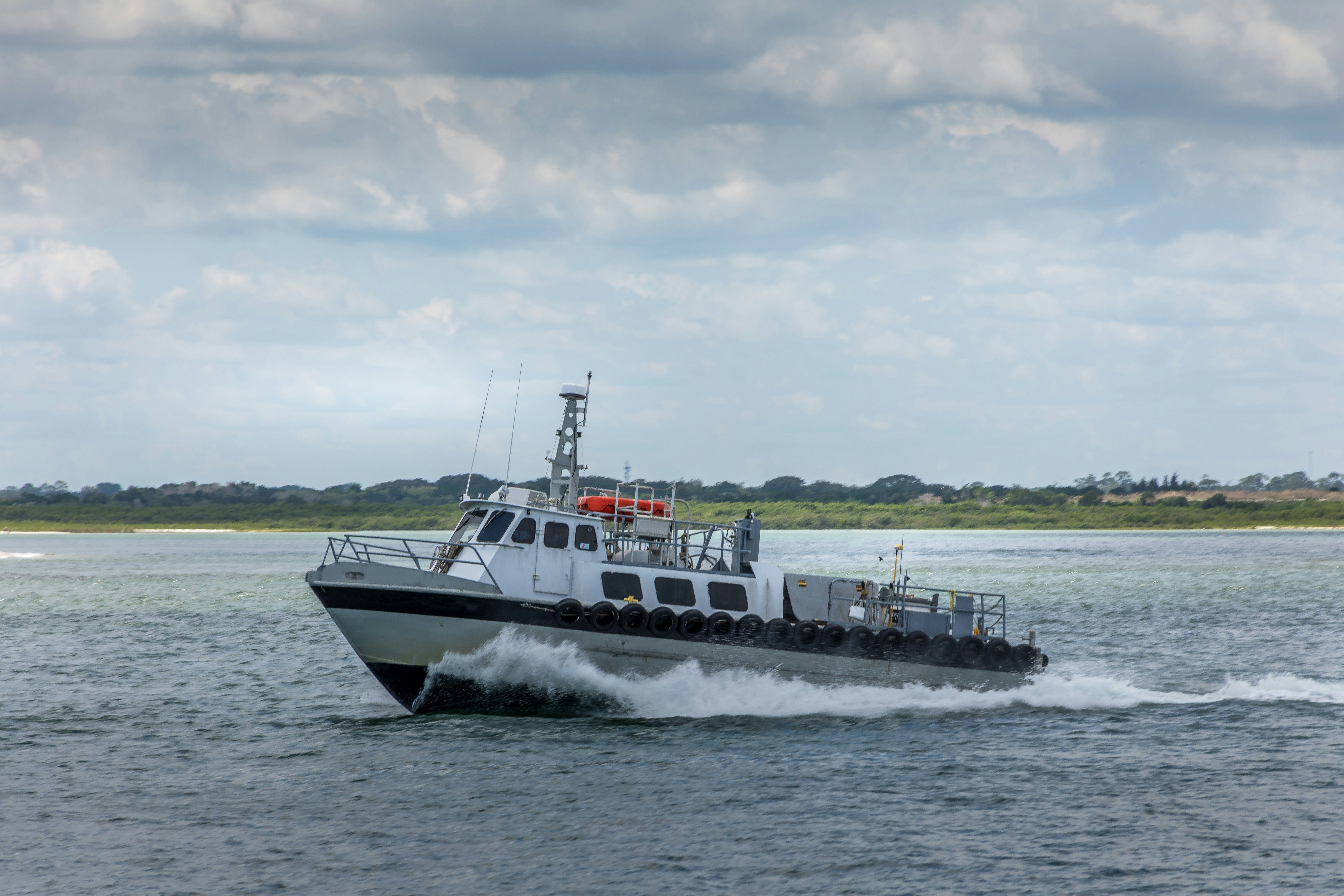 A patrol boat speeds through choppy waters under a cloudy sky near a distant shoreline.