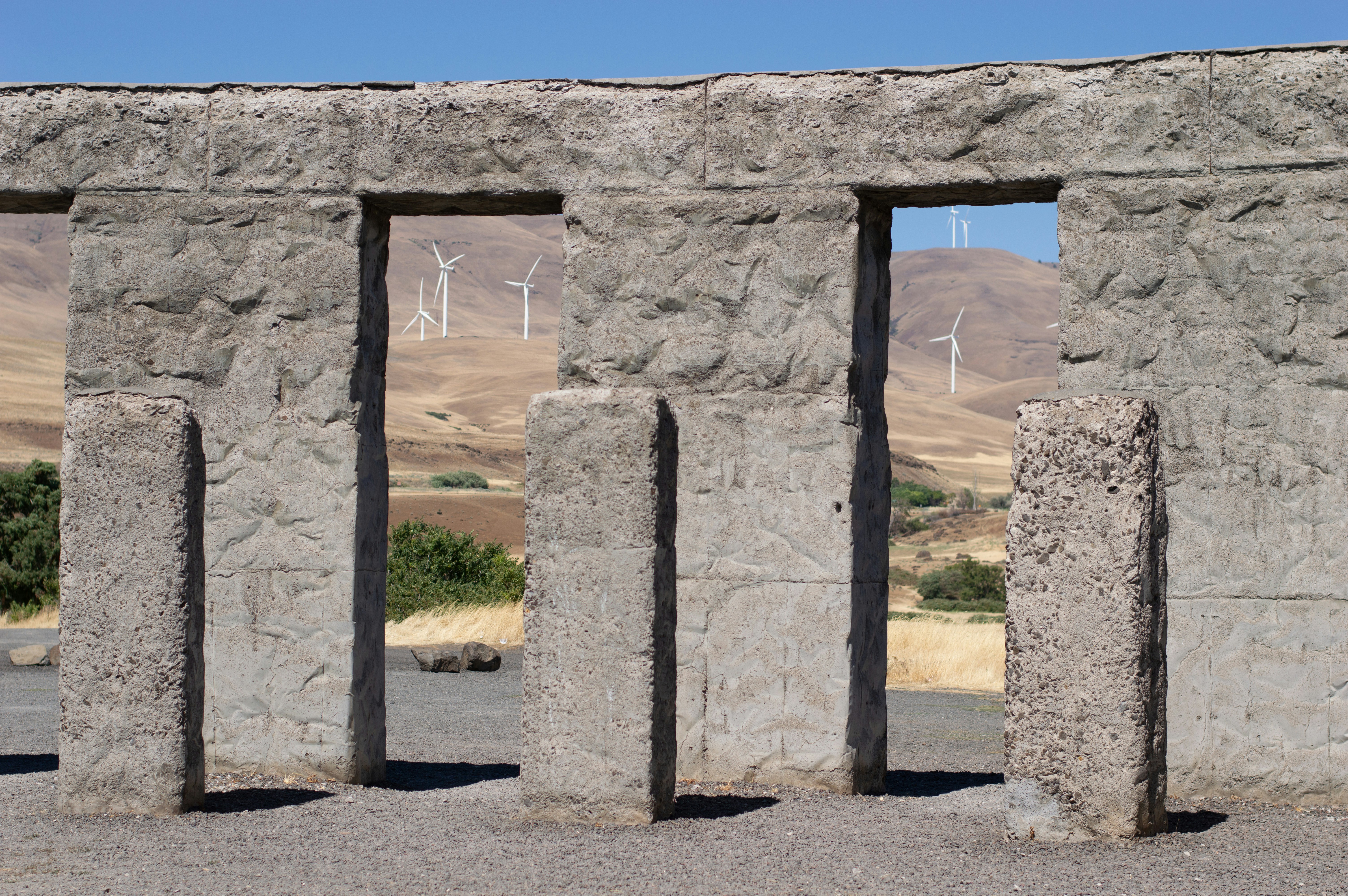 Weathered stone structures frame a distant landscape dotted with wind turbines, illustrating the contrast between history and modernity.