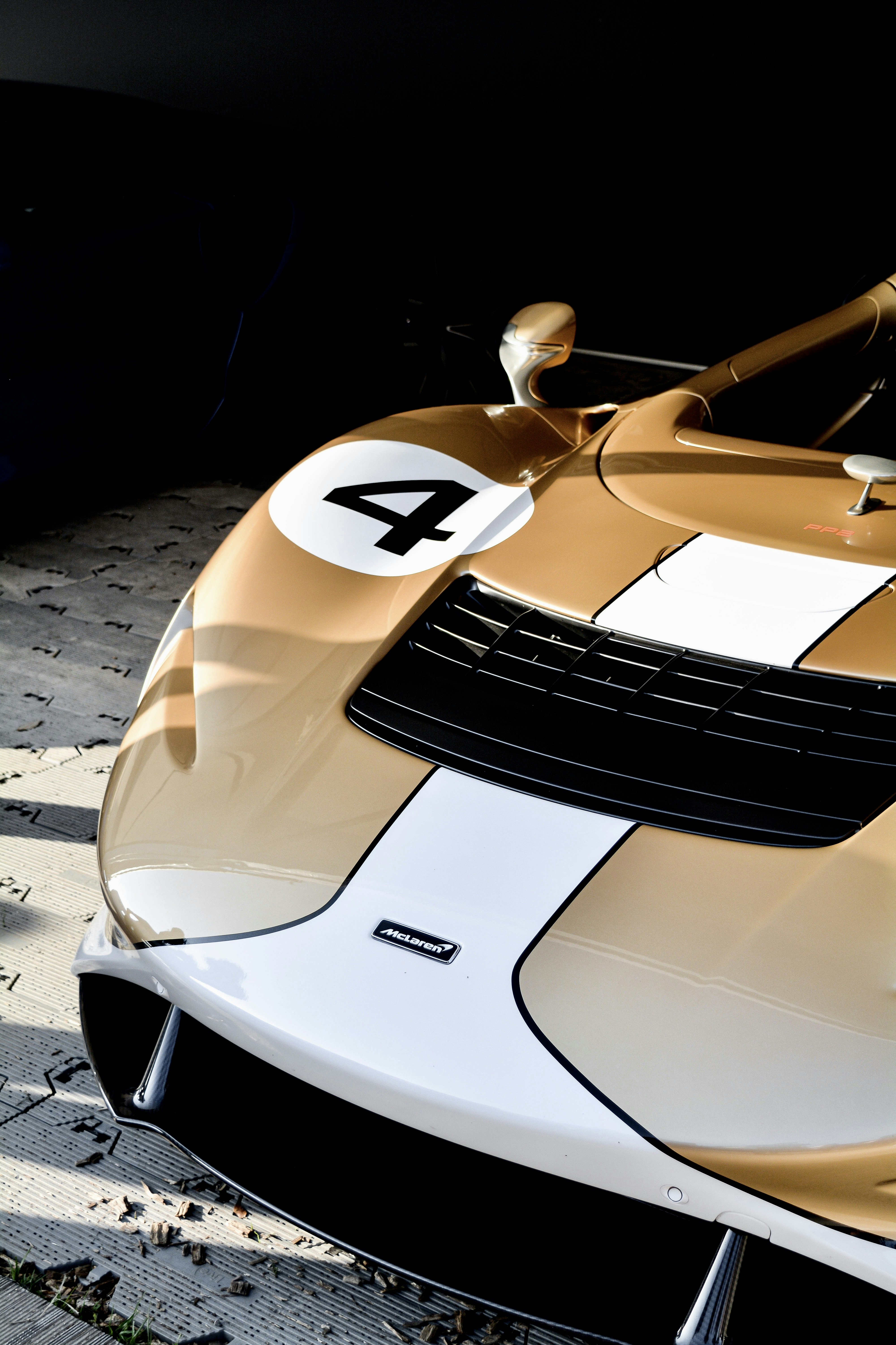 Glossy gold racing car front with white stripes and bold number 4 on hood; shown in a dark setting emphasizing reflected light and chrome details.