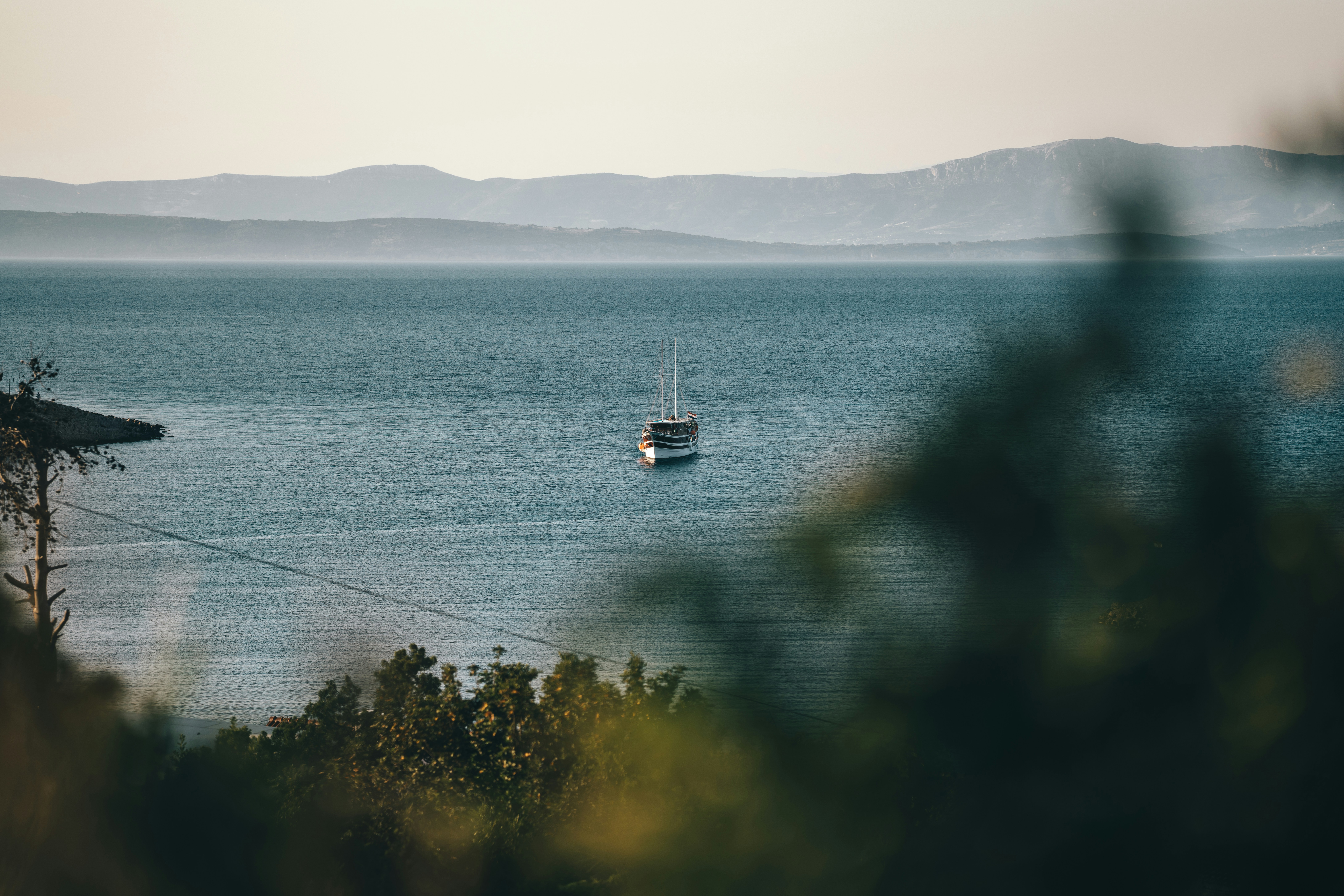 A solitary sailboat glides across a tranquil sea, framed by distant mountains under a soft sky.