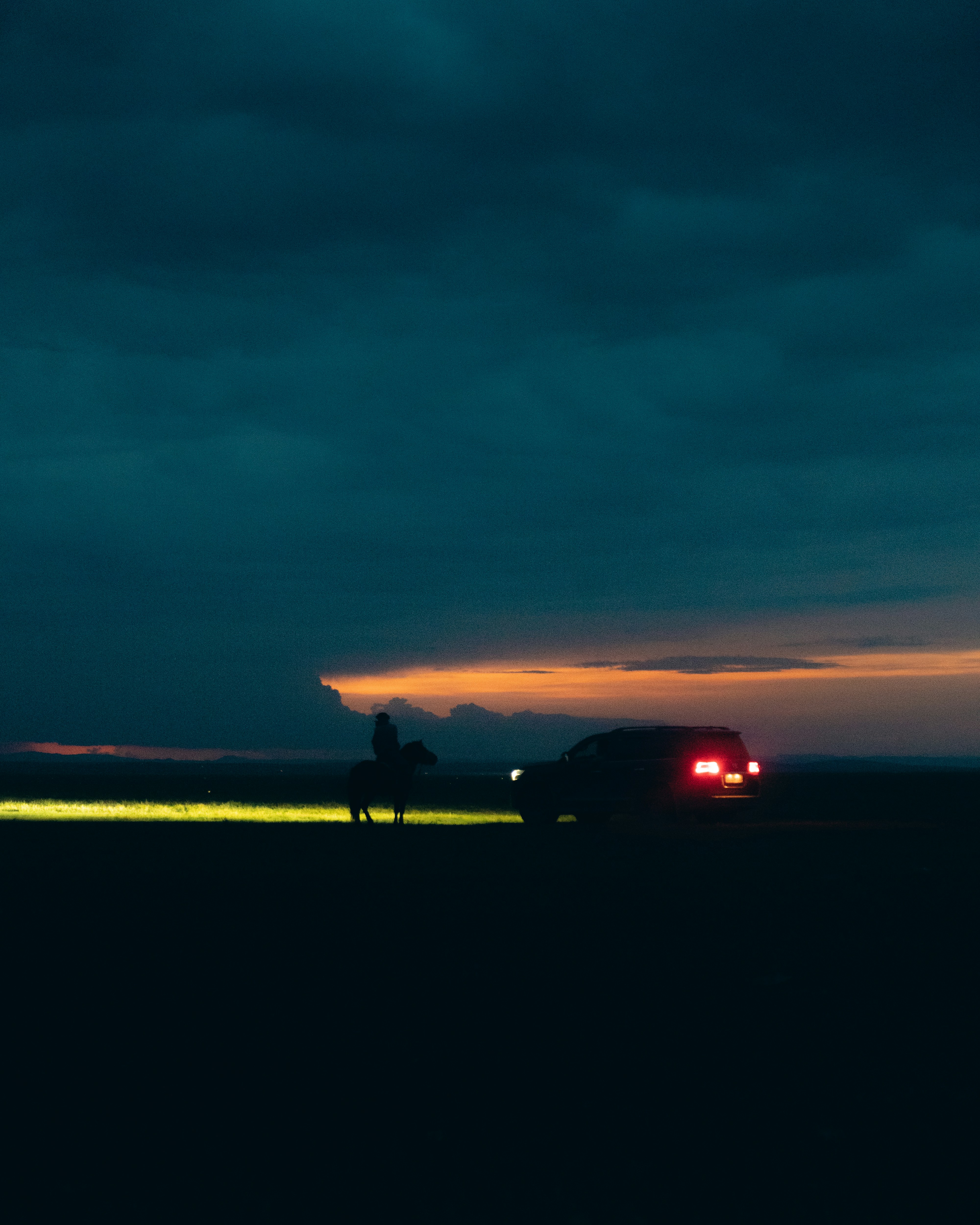Horizon Echoes: A lone rider and a distant car beneath a cobalt dusk