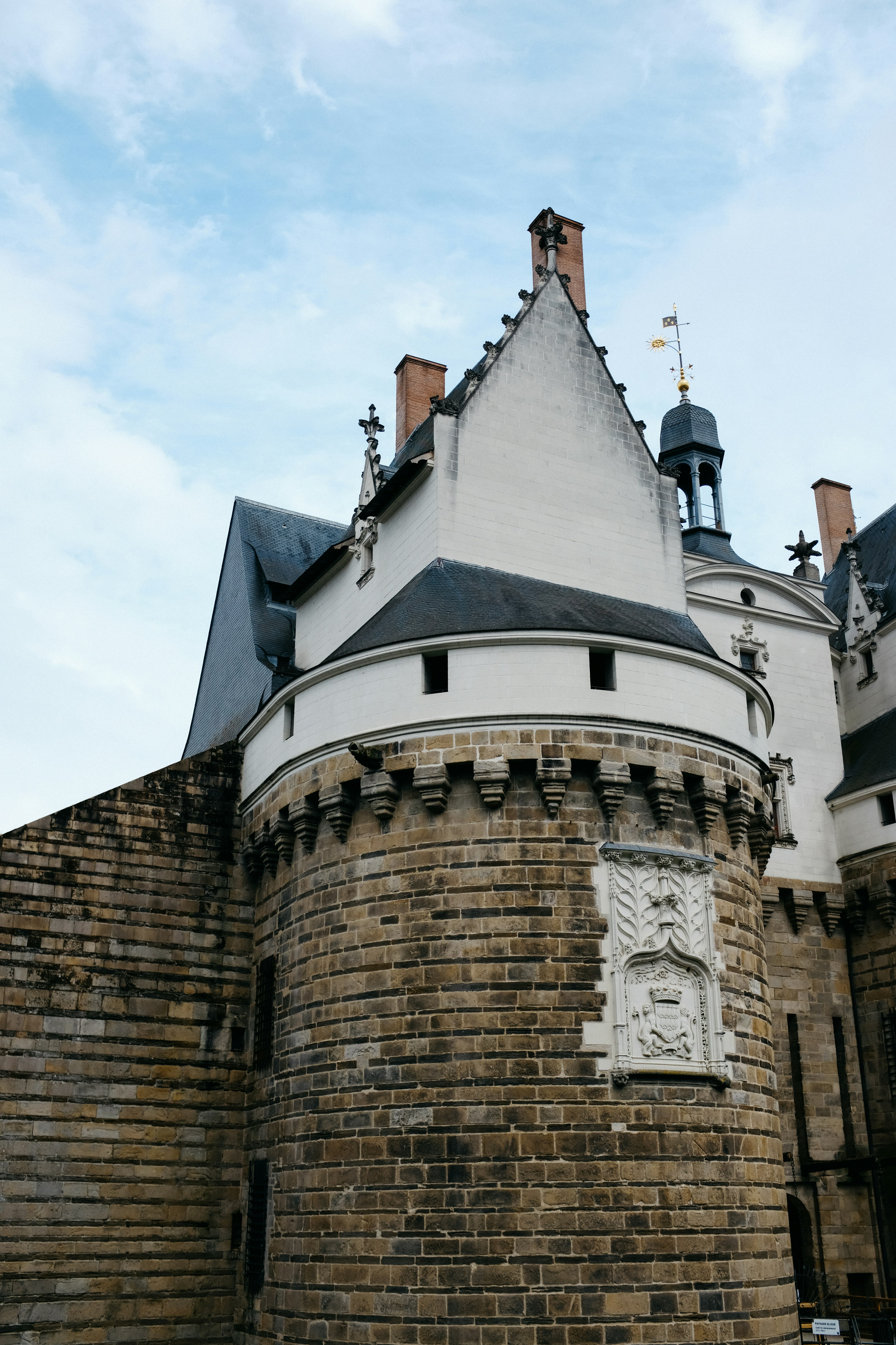 Historic castle architecture featuring a stone tower and intricate rooflines against a cloudy sky.