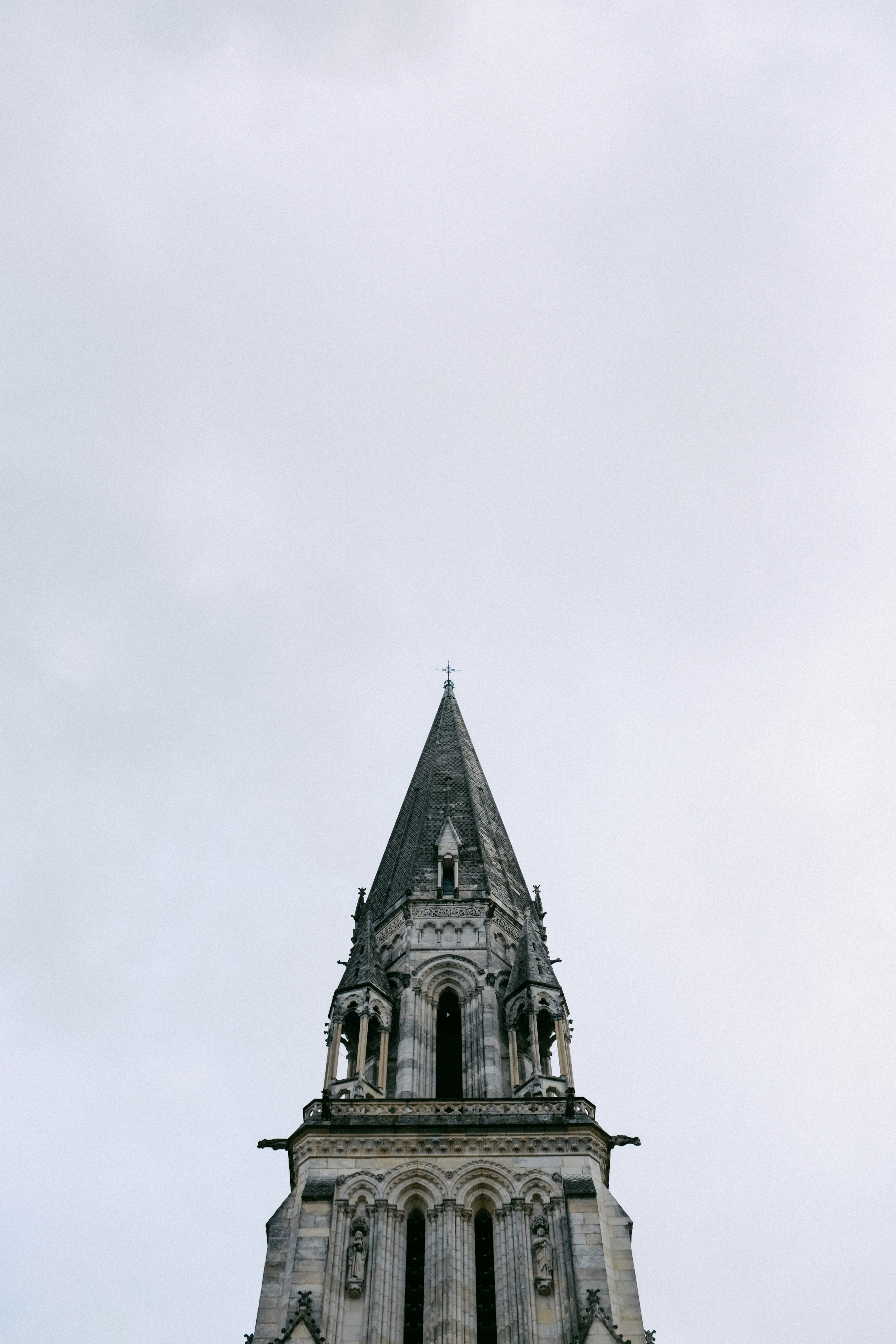 Gothic church steeple piercing the cloudy sky, showcasing intricate stonework and a pointed design.