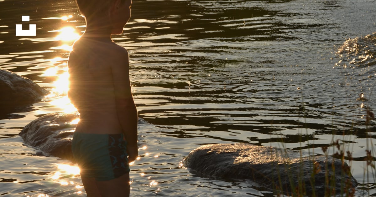昼間に水の上に立って青い半ズボンでトップレスの少年の写真 Unsplashの無料日の出写真