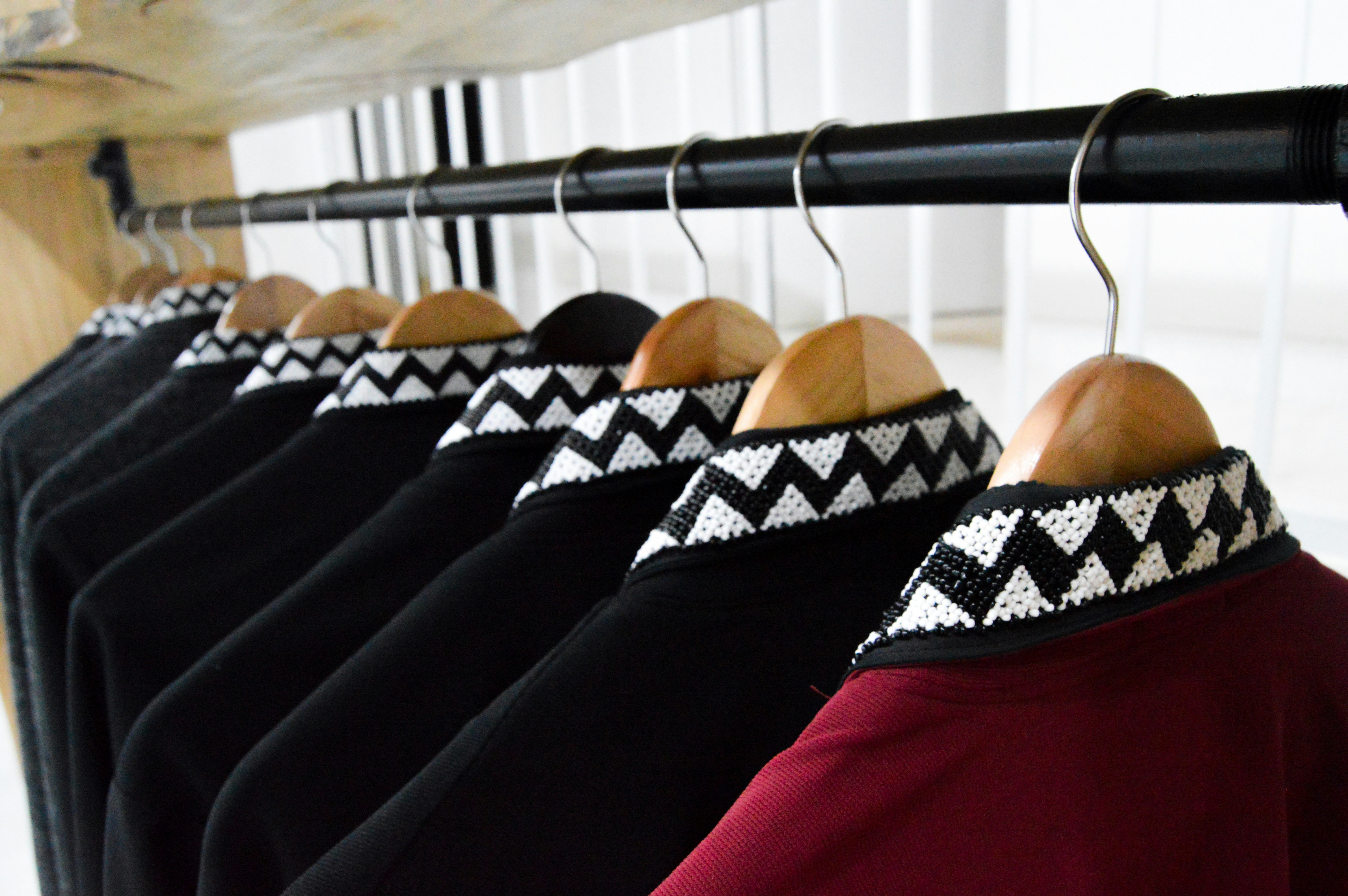 Traditional garments with geometric patterned collars hanging on wooden hangers in a bright store display.