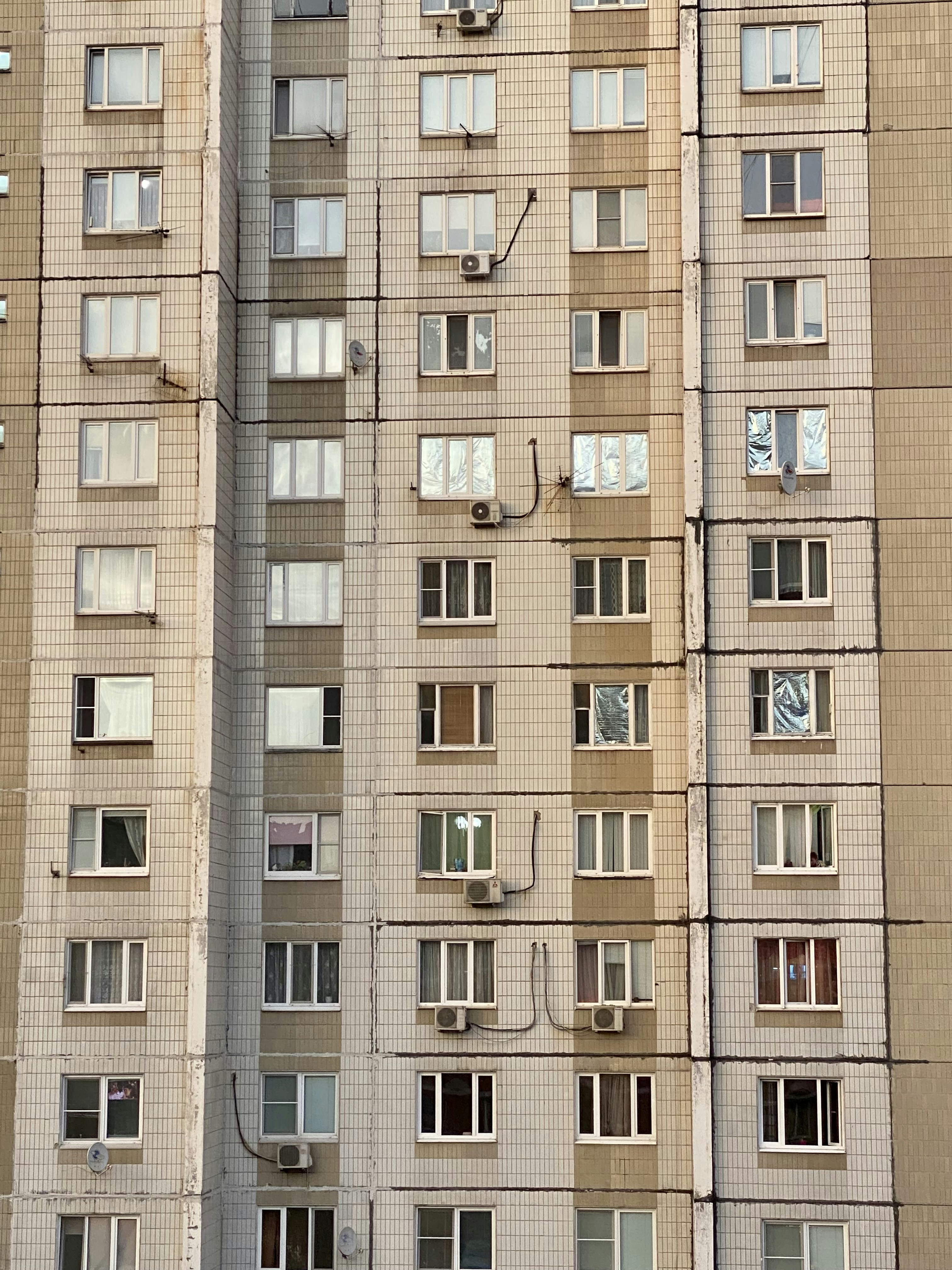Close-up view of a residential building's exterior, showcasing a grid of windows and air conditioning units. The facade features a mix of colors and textures.