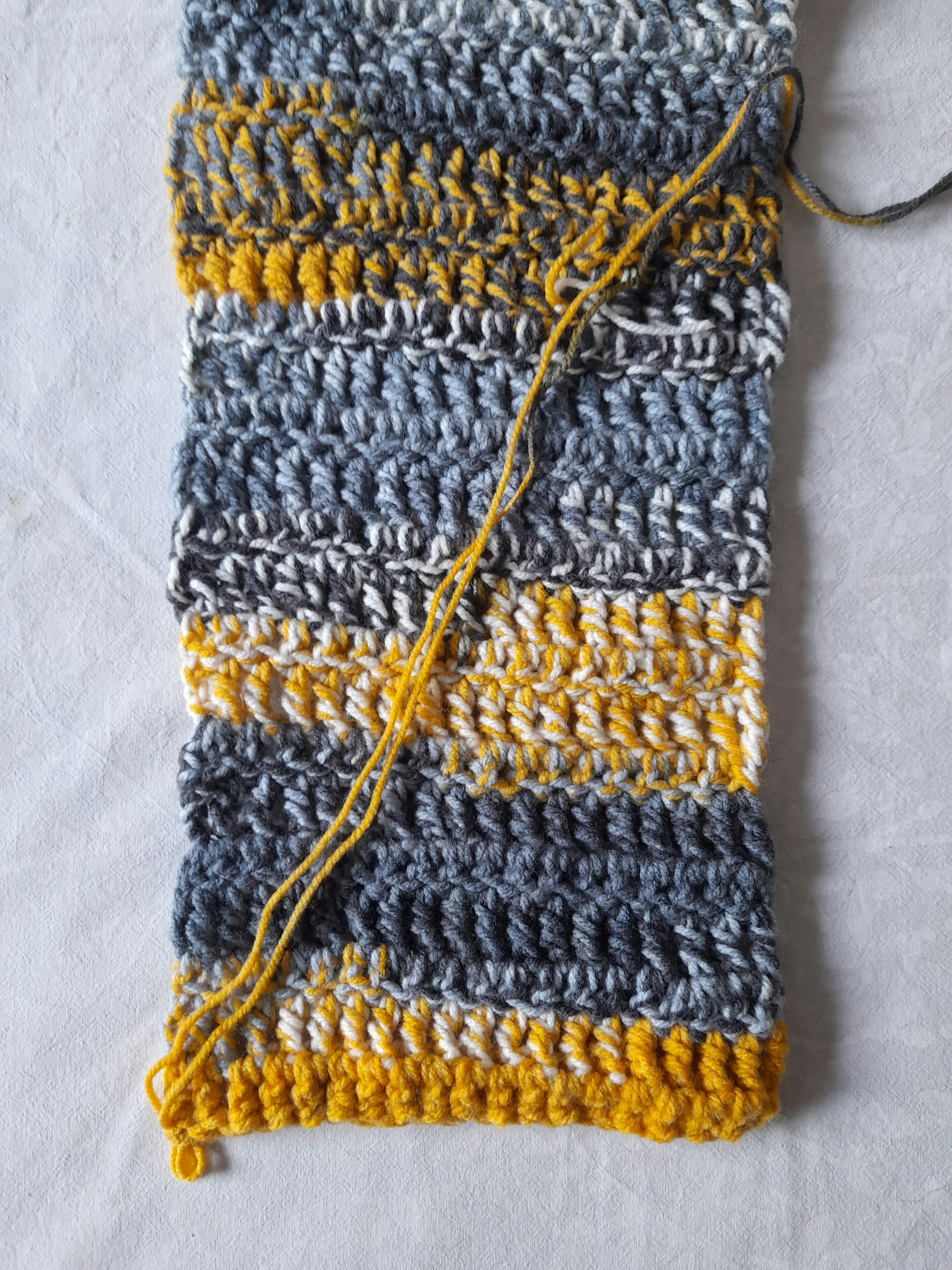 Close-up of a striped knitted fabric in gray and yellow tones on a white background, with a bright yellow thread crossing the weave.