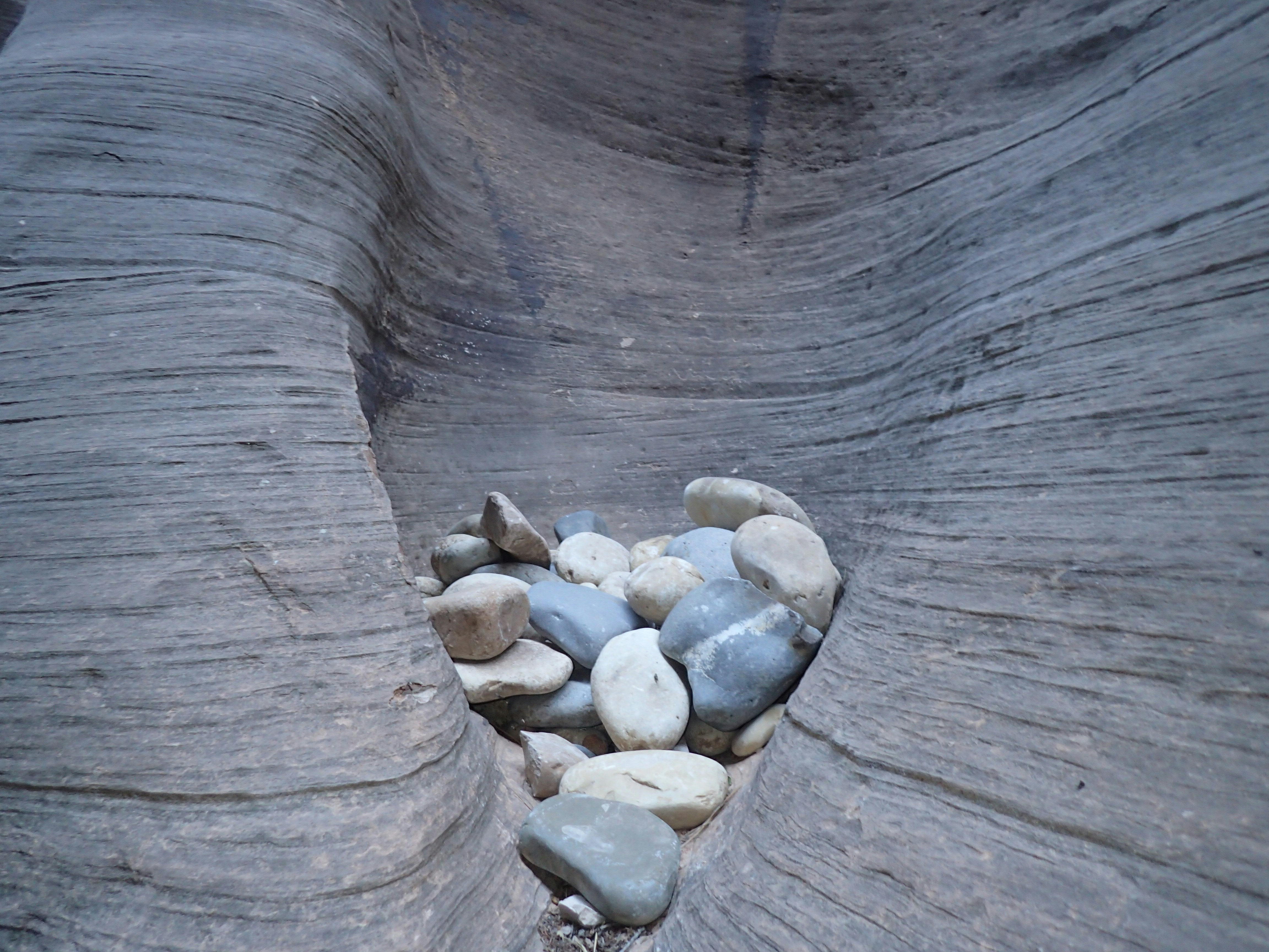 Smooth pebbles nestled in a natural rock formation, showcasing the beauty of erosion and time. The intricate textures of the surrounding stone create a serene atmosphere.