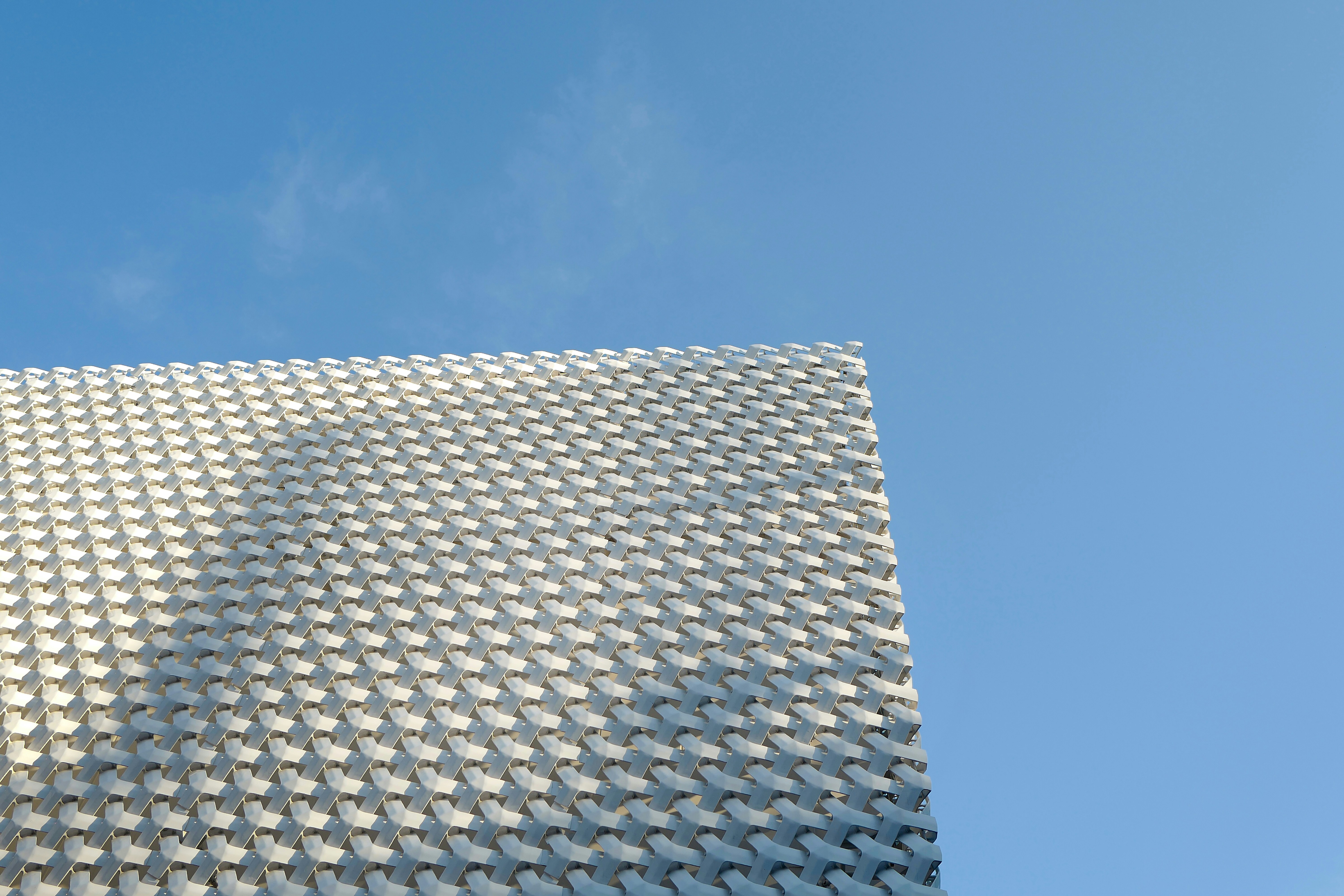 Textured facade of a modern building set against a bright blue sky, showcasing intricate geometric patterns.
