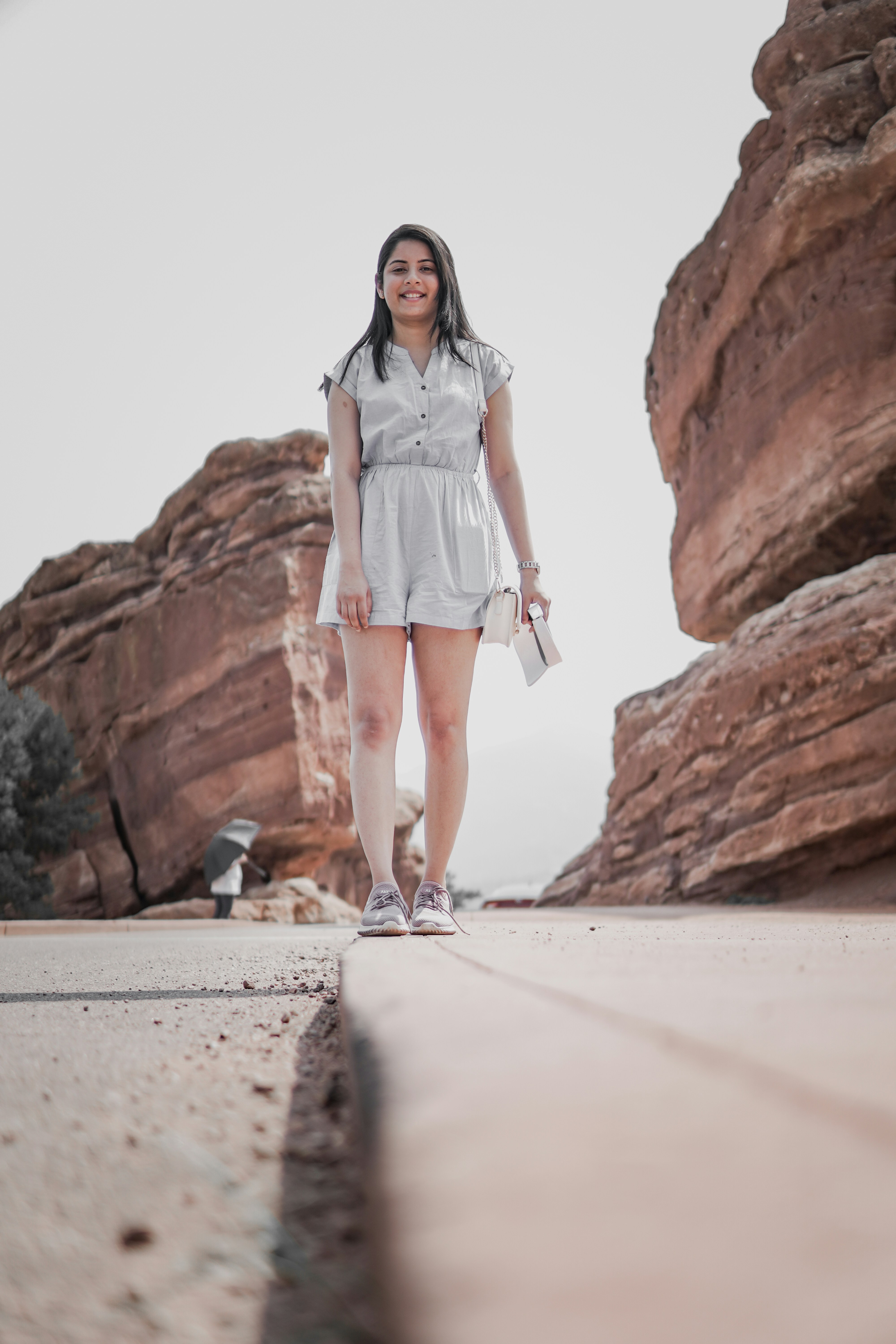Woman in white dress shirt and white skirt standing on brown rock ...