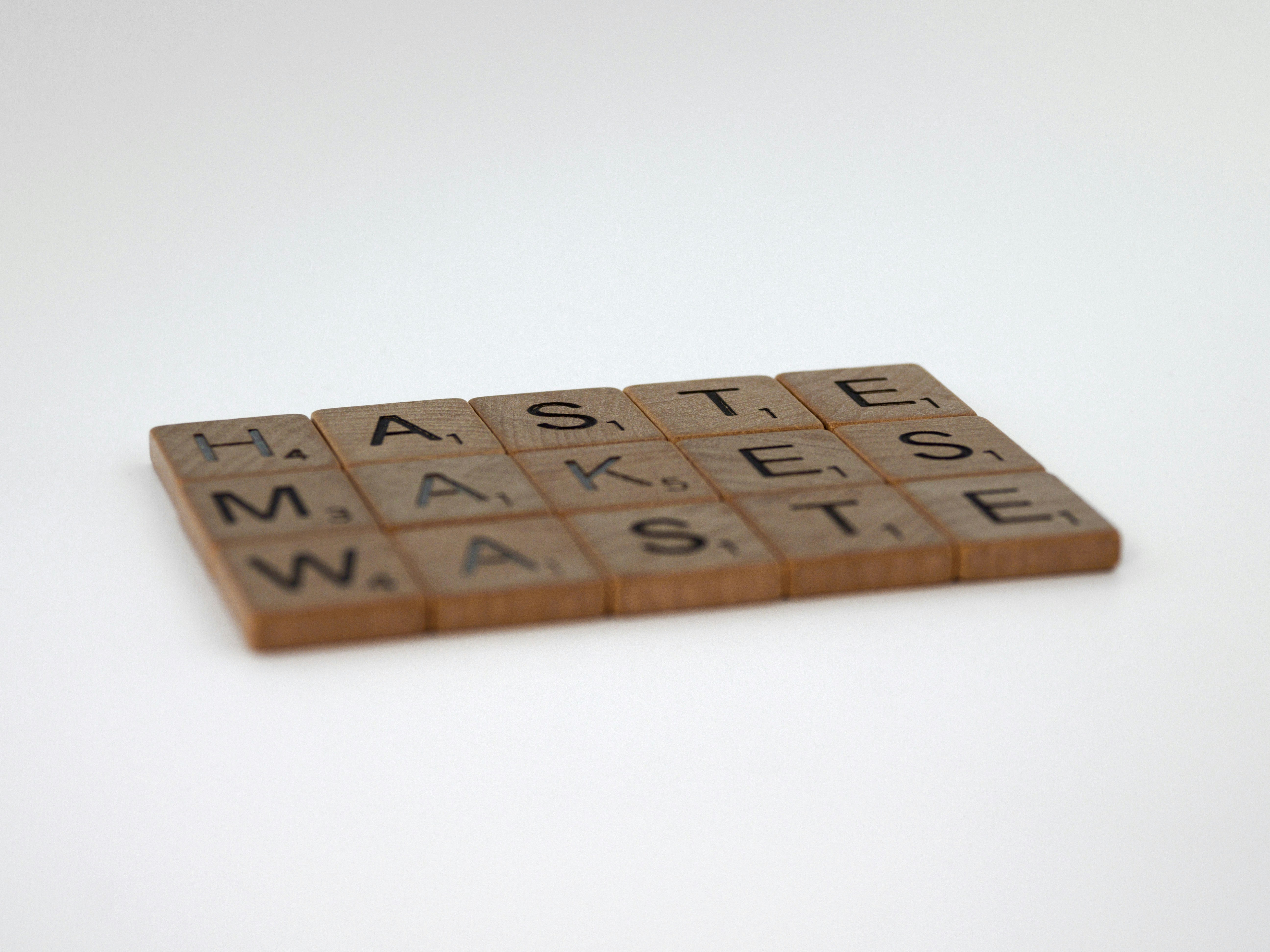 Proverb Mosaic: Wooden Scrabble Tiles Spell 'HASTE MAKES WASTE' on a Minimal Studio Backdrop