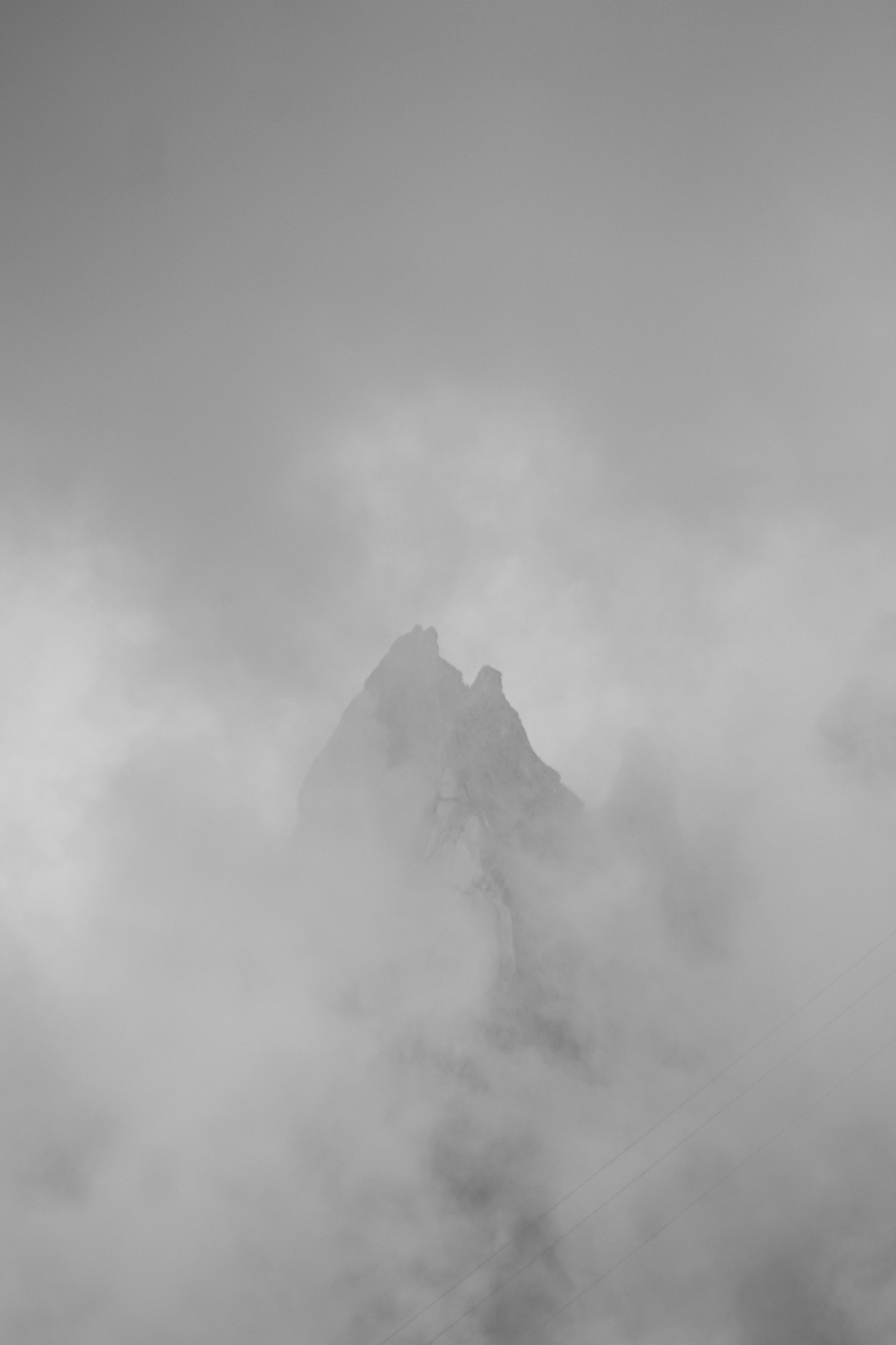 A jagged mountain peak emerges through a veil of swirling clouds, creating a mysterious and ethereal atmosphere.
