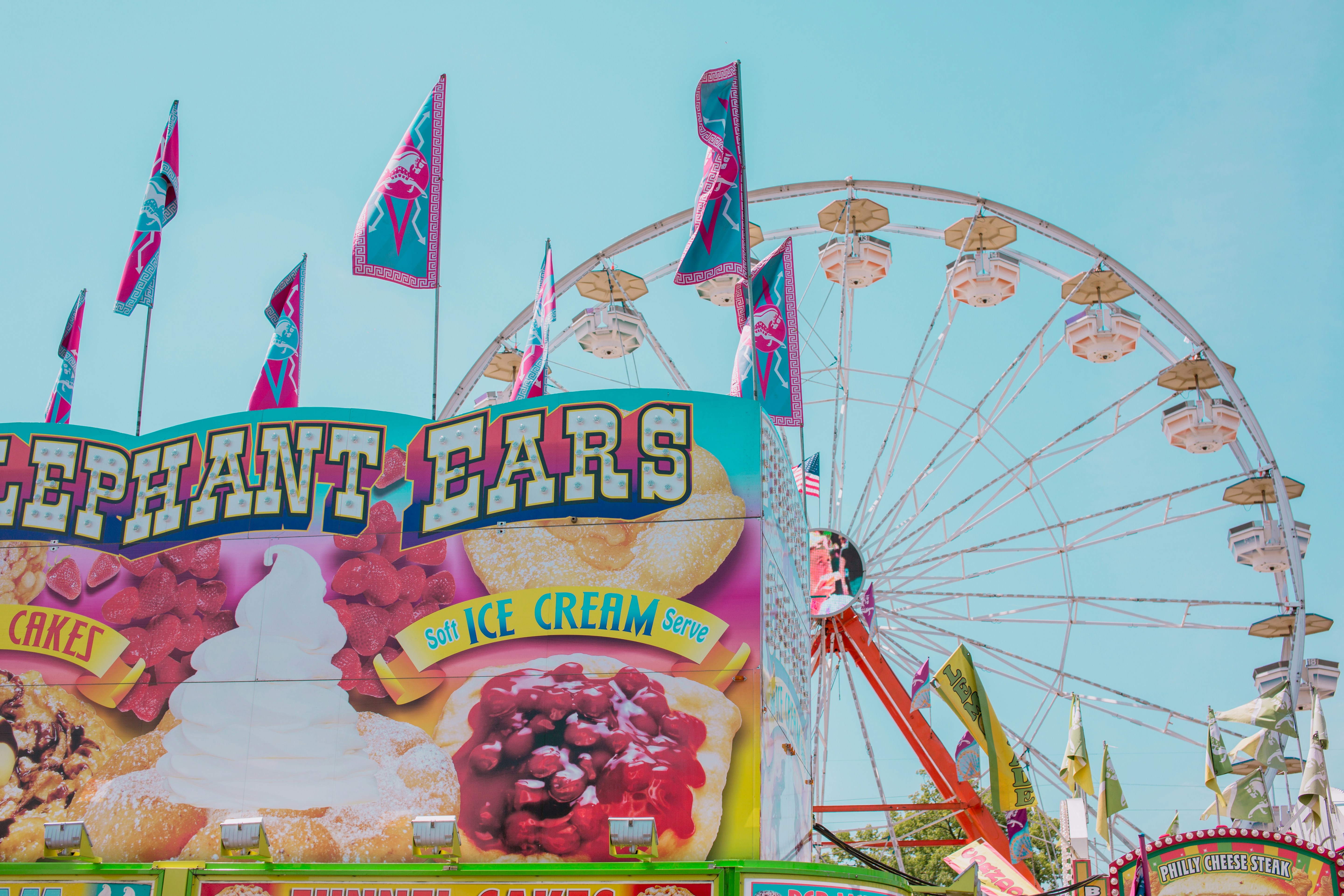 Elephant Ears Signage at a Sunlit Carnival with a Ferris Wheel in the Background