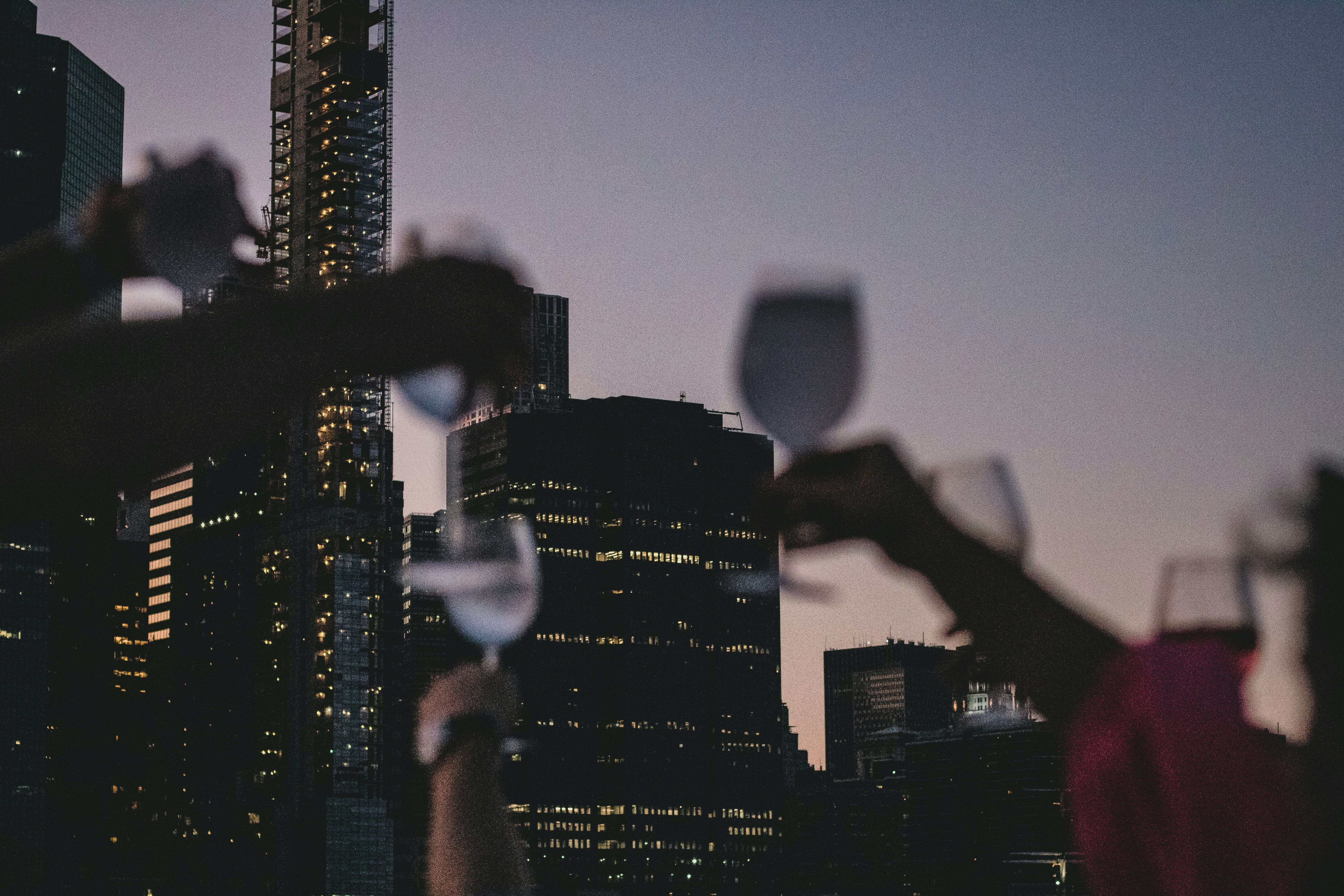 Toast above the skyline: glasses lifted against evening cityscape